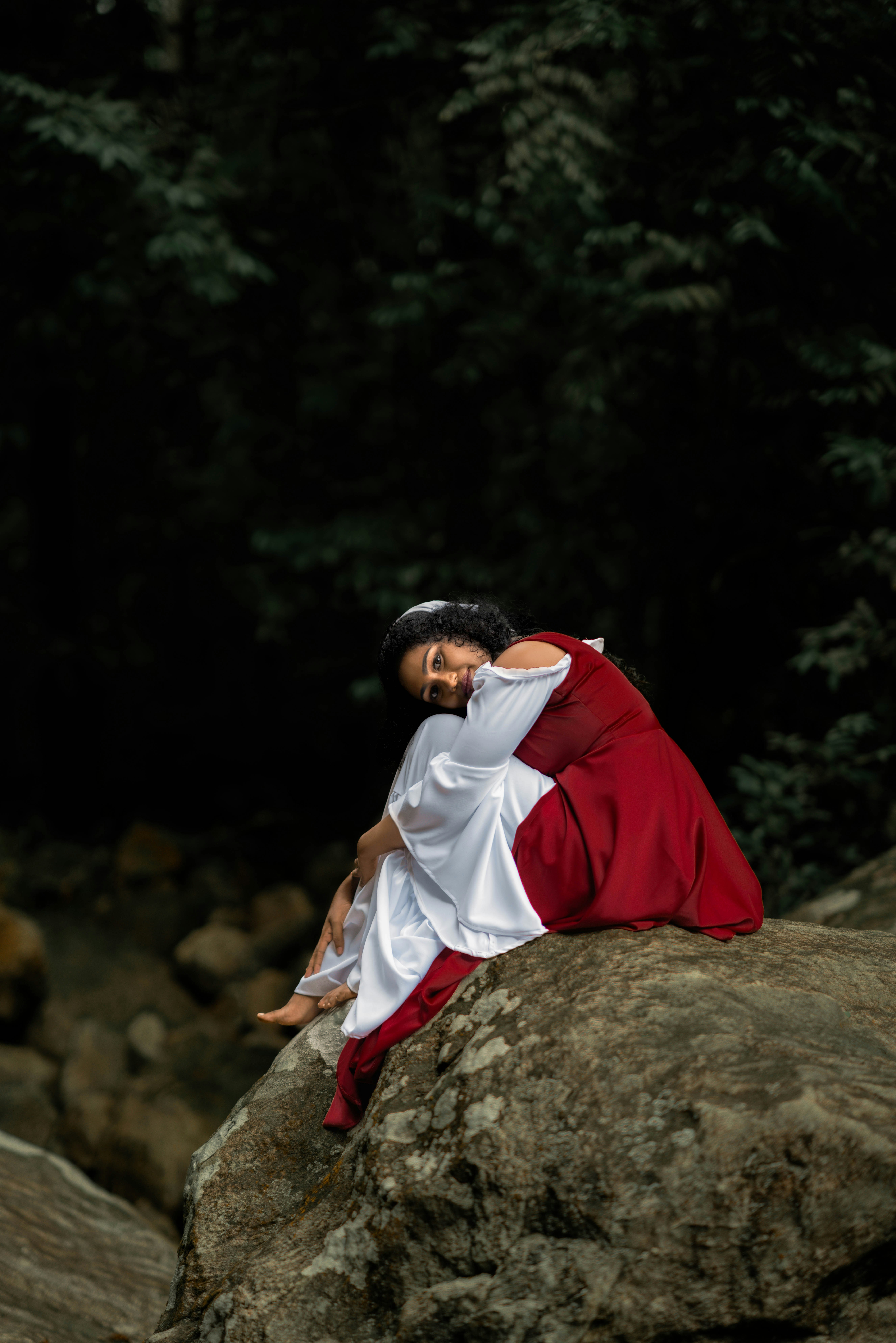 Person in red and white robes sitting on a rock.
