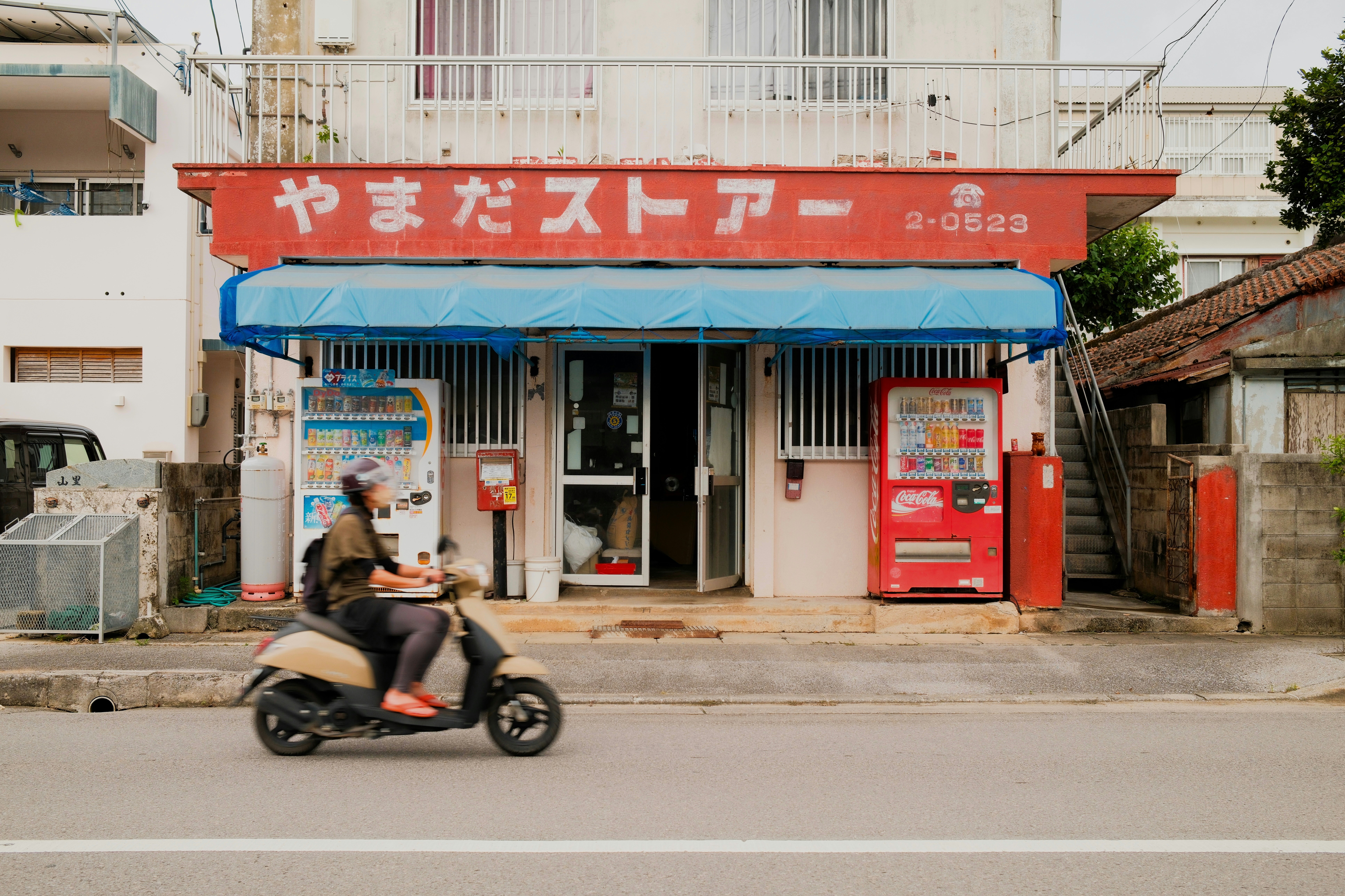 Blue Canopy Convenience, Red Vending, and a Moving Rider