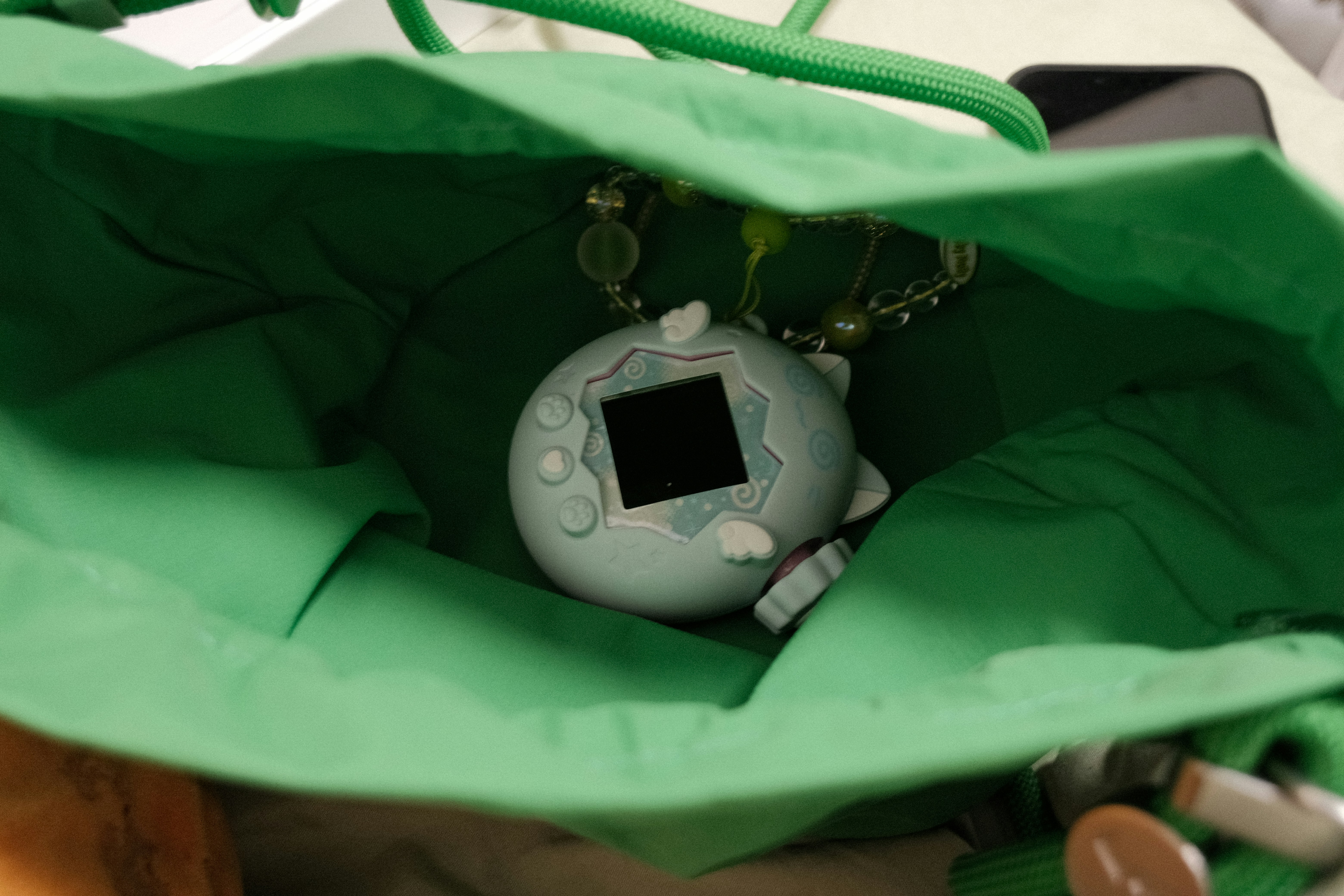 A light blue tamagotchi virtual pet inside a green bag.