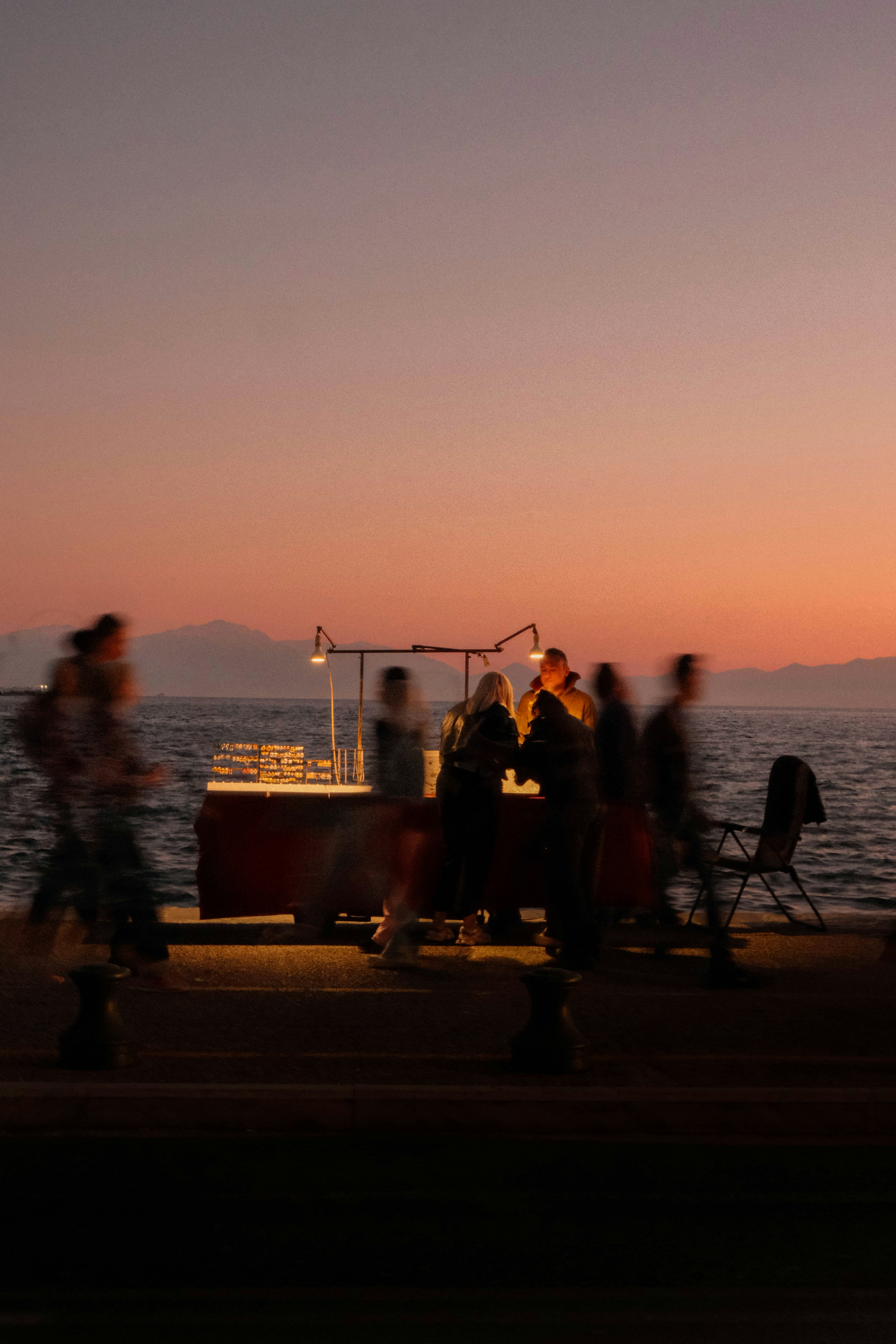 Sunset over a seaside food cart with blurred people.