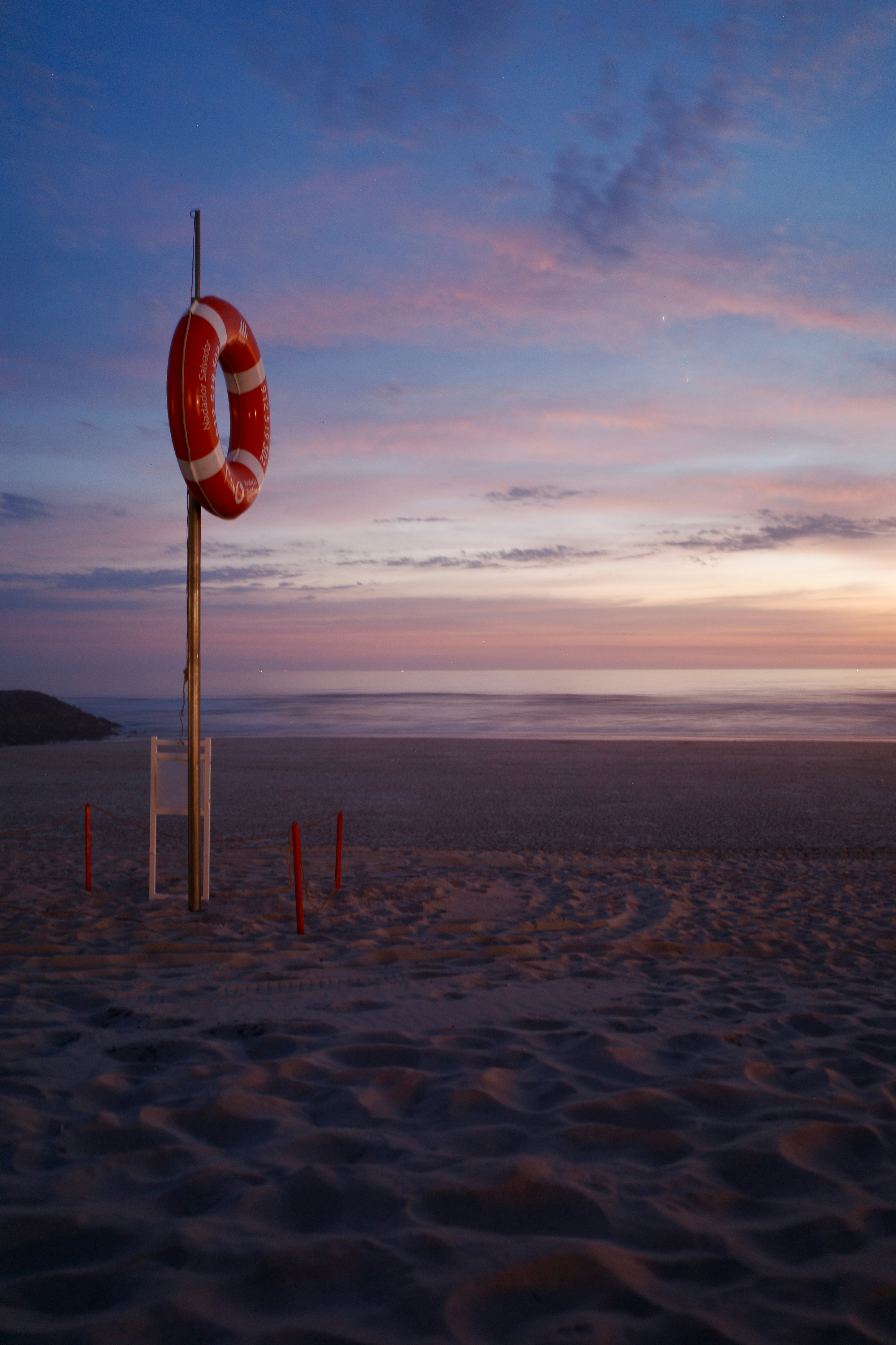 Lifebuoy on a sandy beach under a colorful sunset sky.