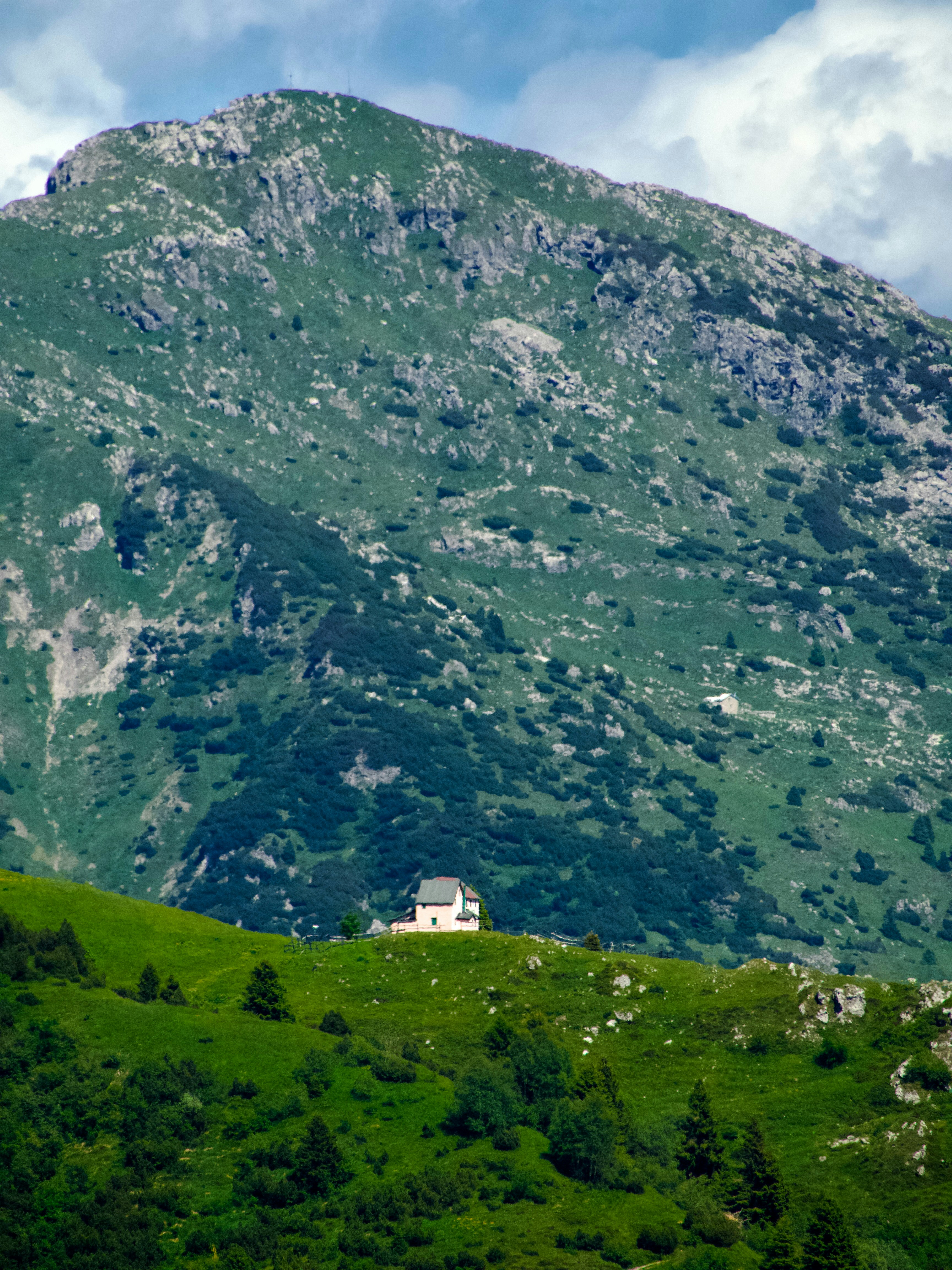 Small white house rests on a grassy hillside with rugged mountain slopes in the background.