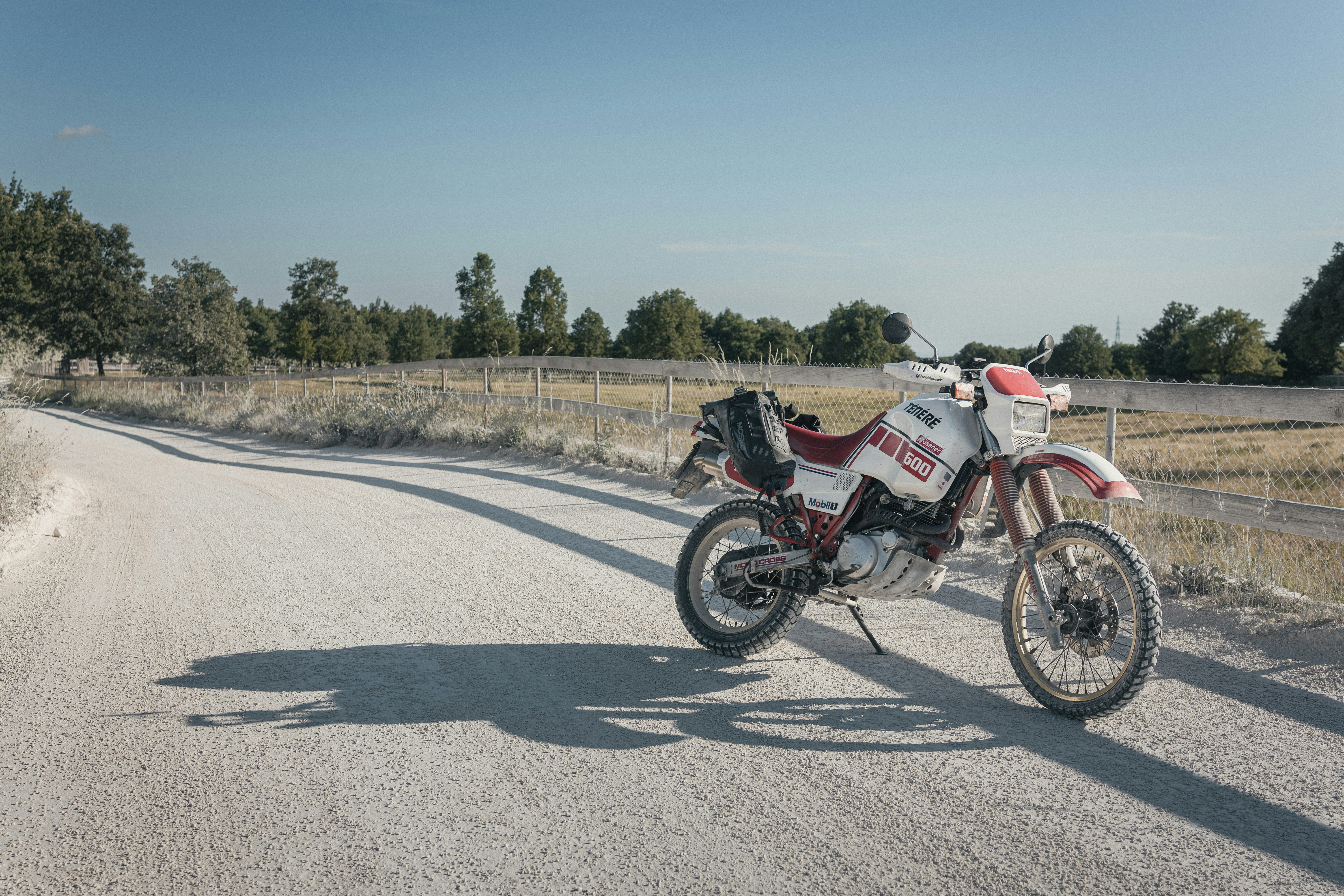 Dusty Roadside Guardian: A Red and White Enduro Standing by the Quiet Rural Track