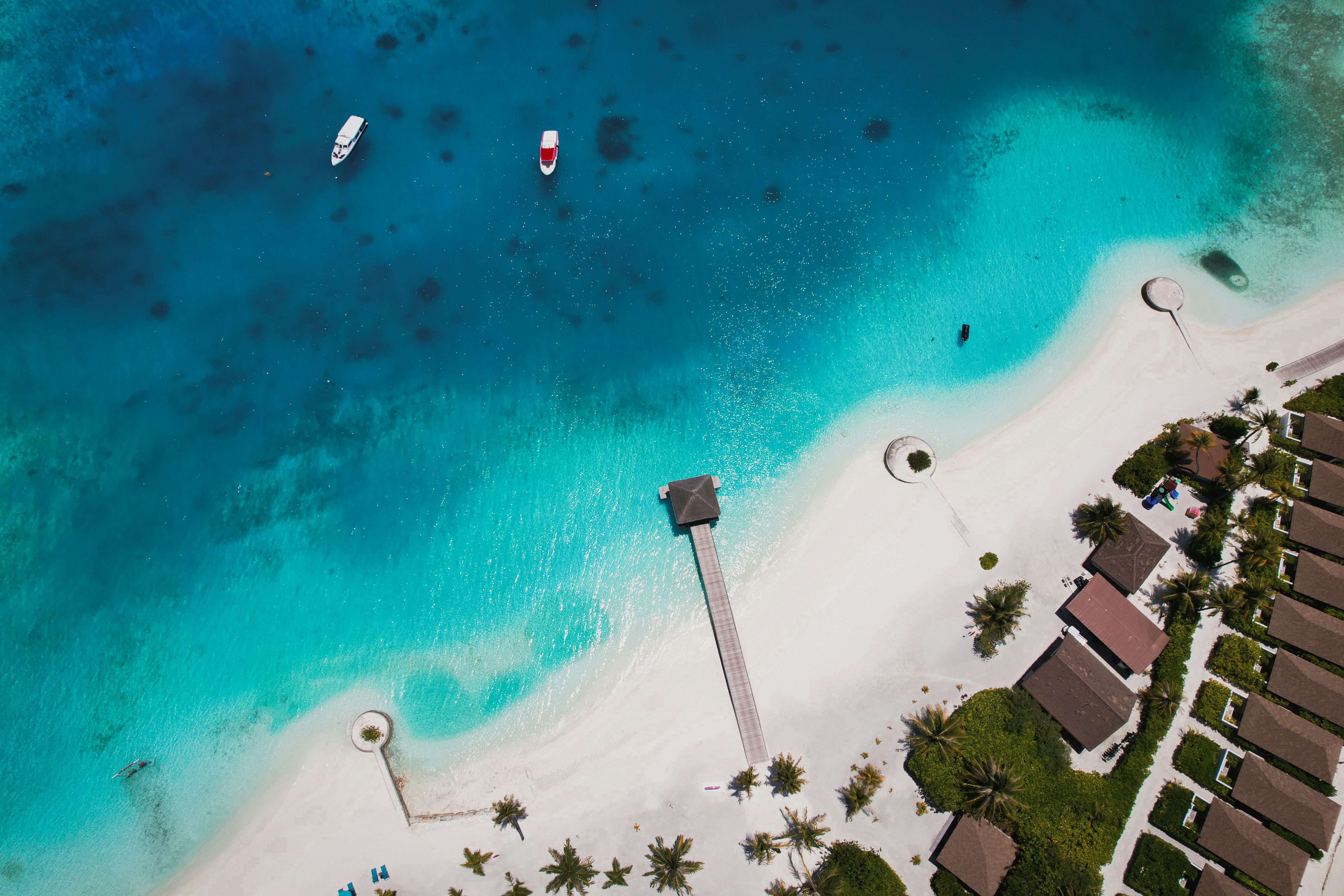 Aerial view of tropical beach, turquoise ocean, pier, and boats.