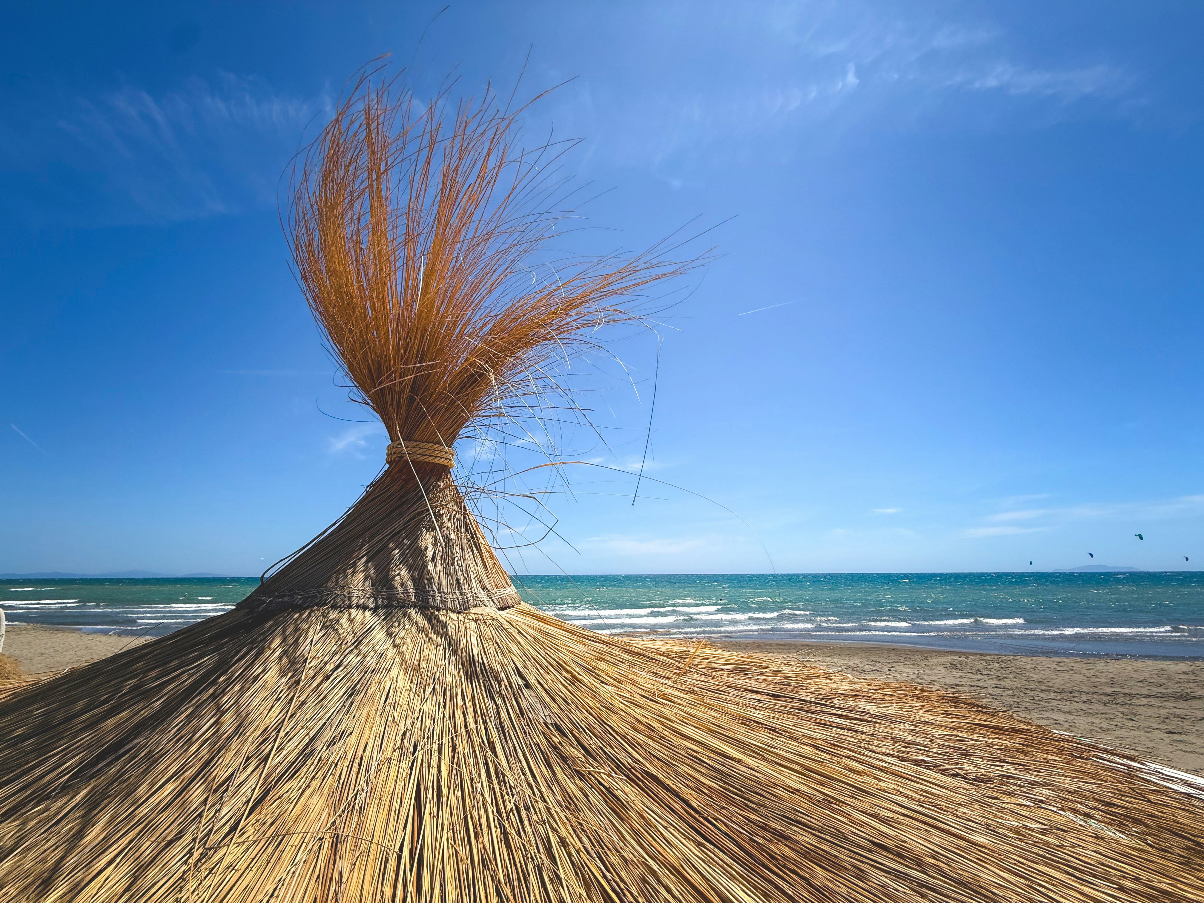 Straw beach umbrella against a blue sky and ocean.