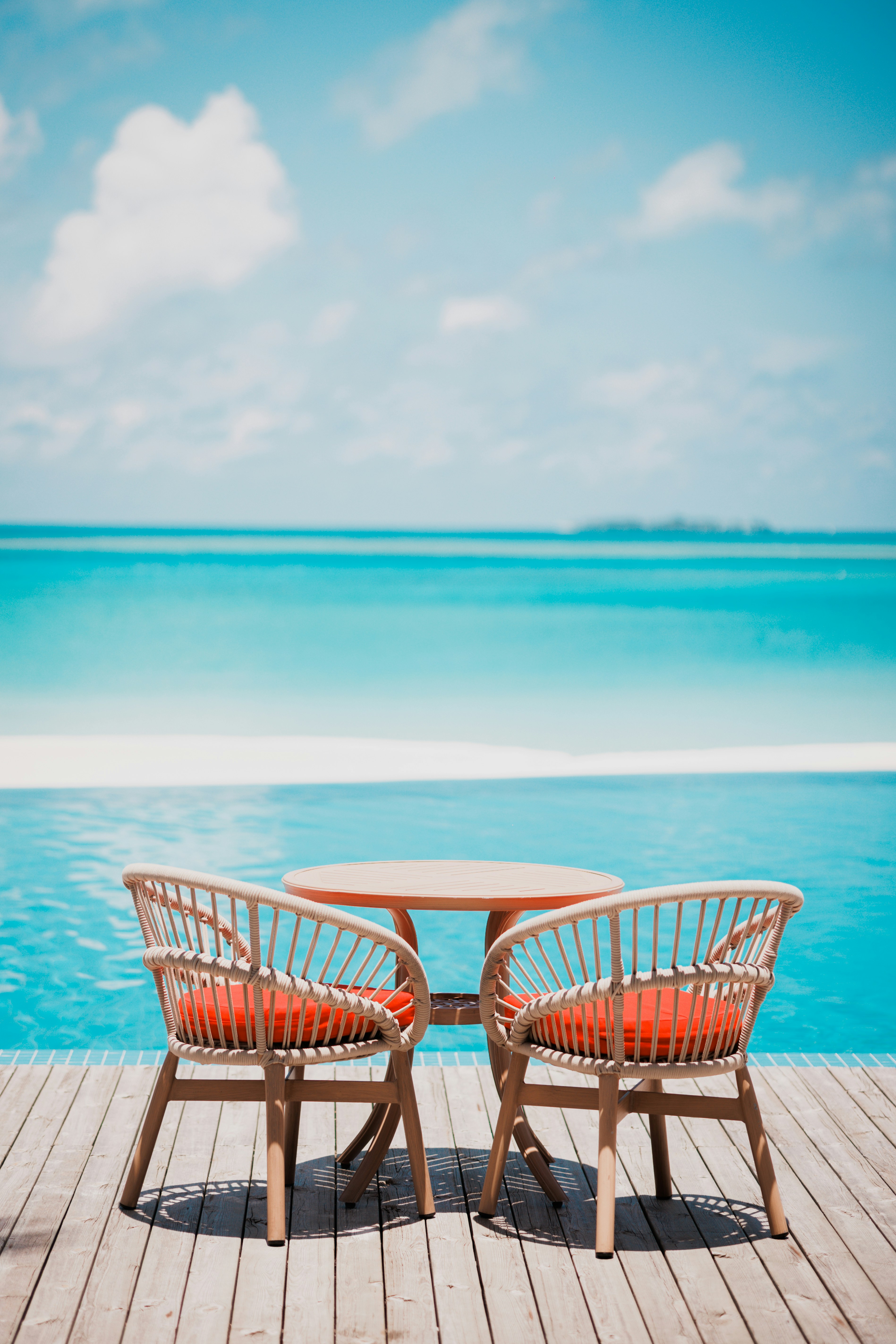Chairs and table by infinity pool overlooking turquoise ocean.