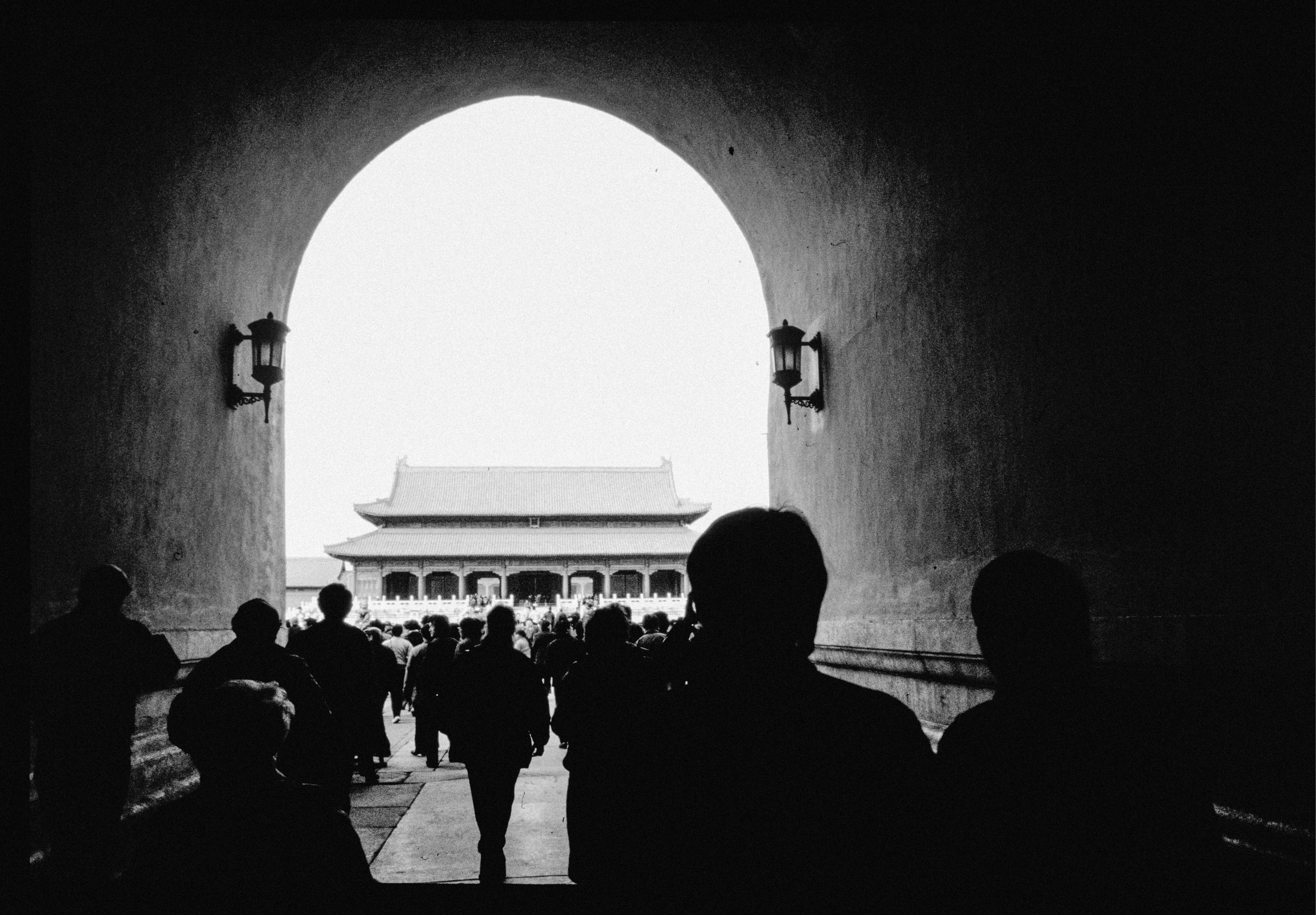 Silhouetted crowd walks through an archway towards a traditional building.