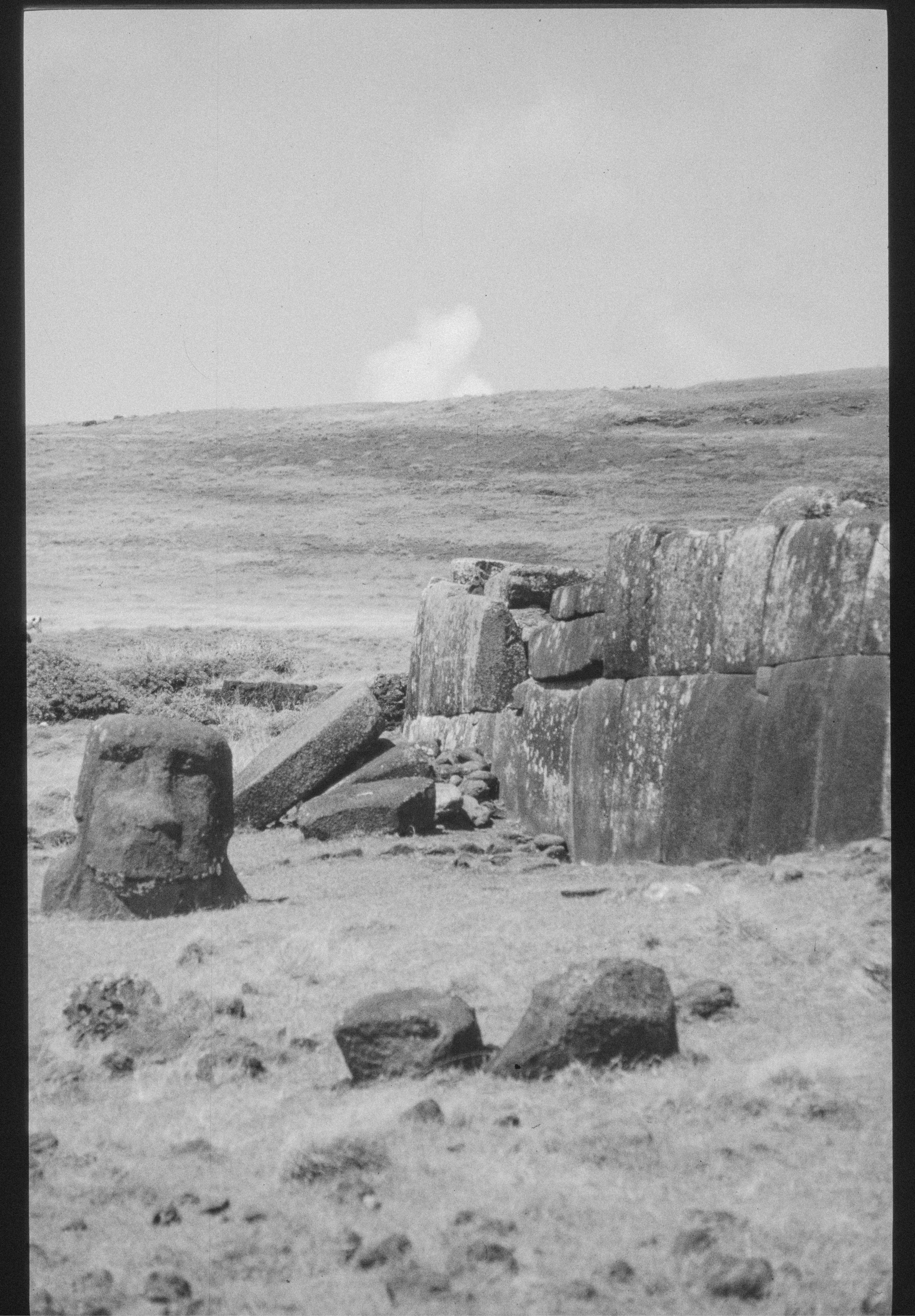 Ancient moai statue and stone ruins on a grassy field.