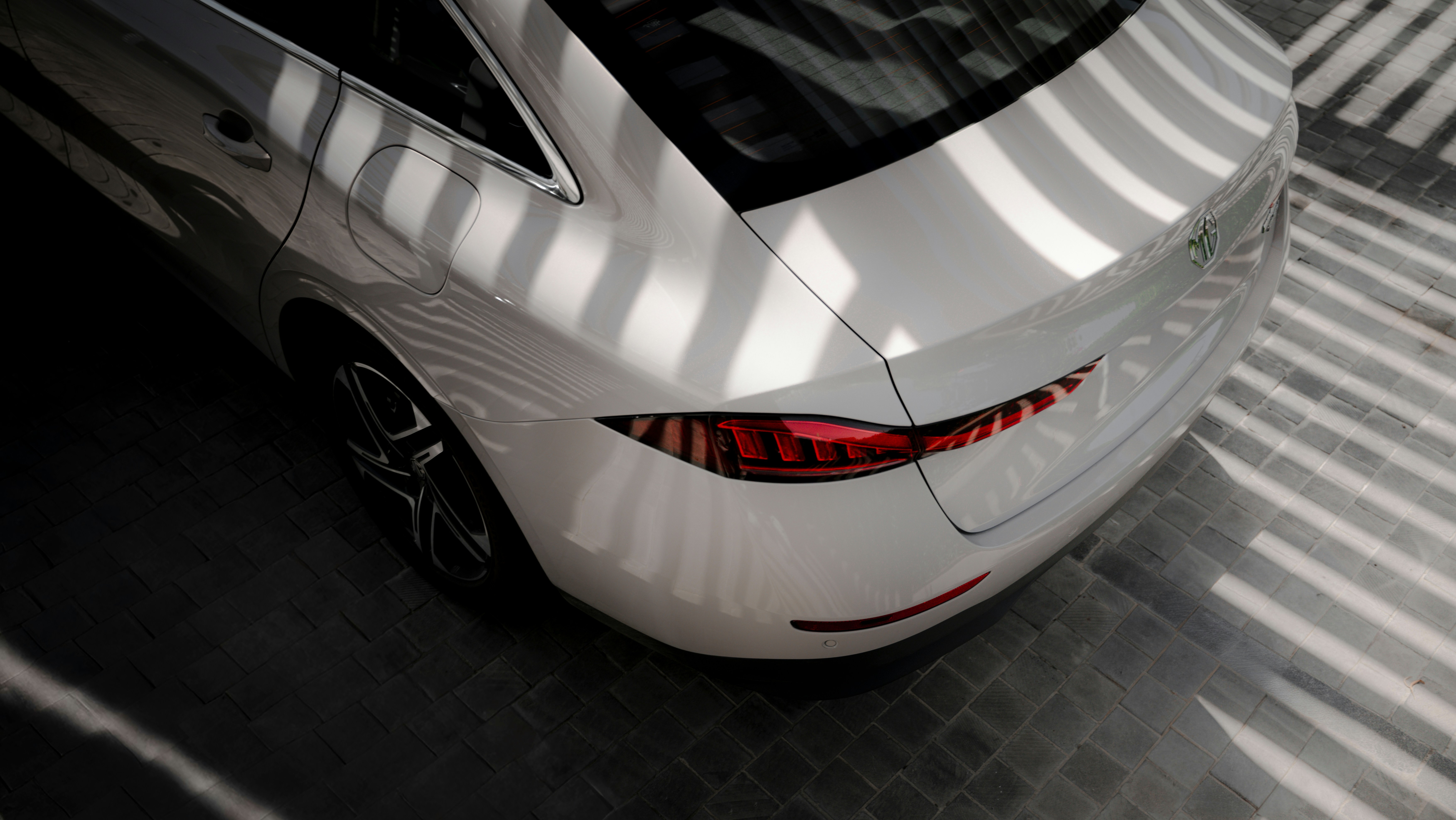Shimmering rear silhouette: a sunlit Aston-like sedan under striped reflections