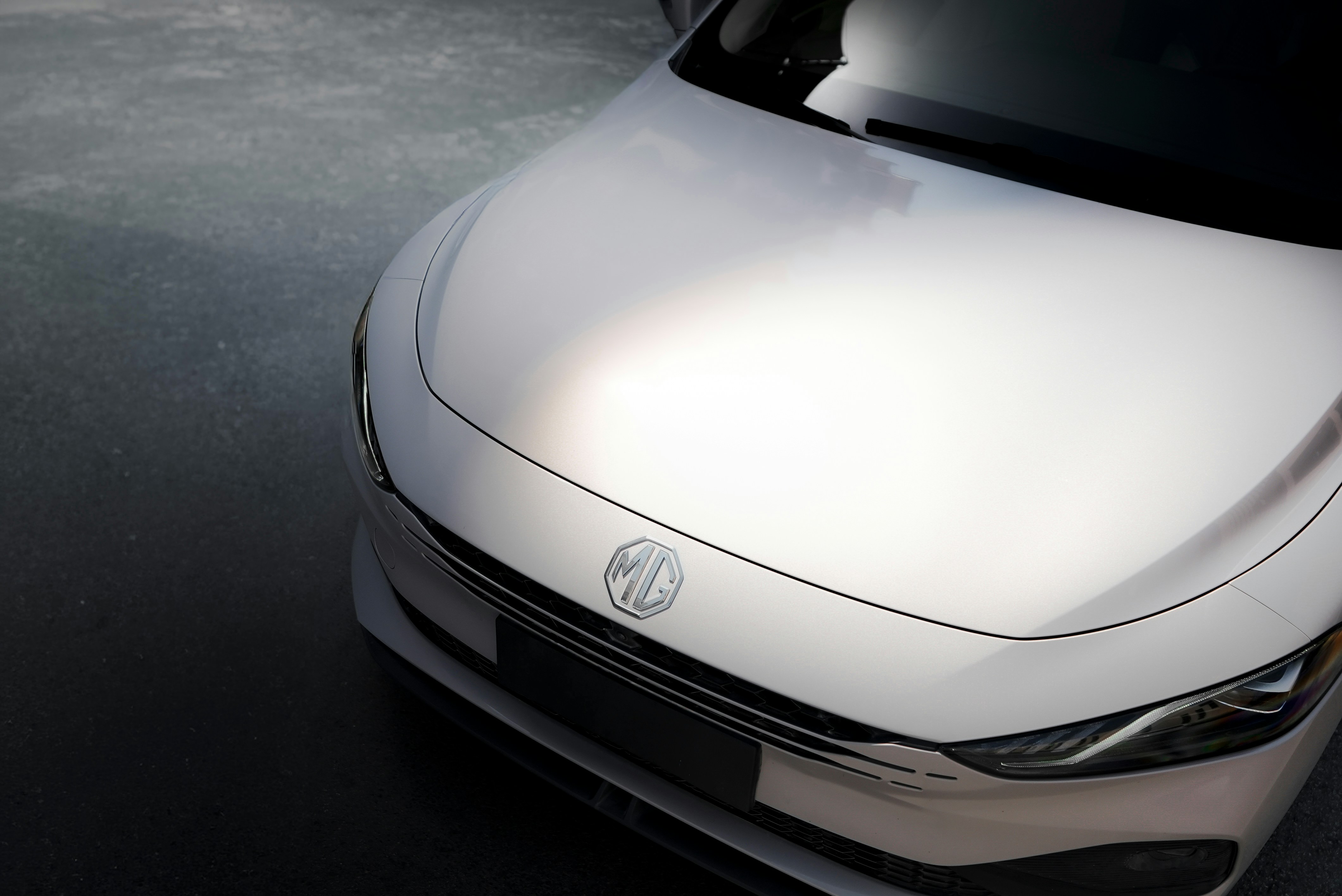 Silver MG hood gleams under soft, diffuse light, emphasizing the chrome grille and badge against a dark asphalt backdrop.