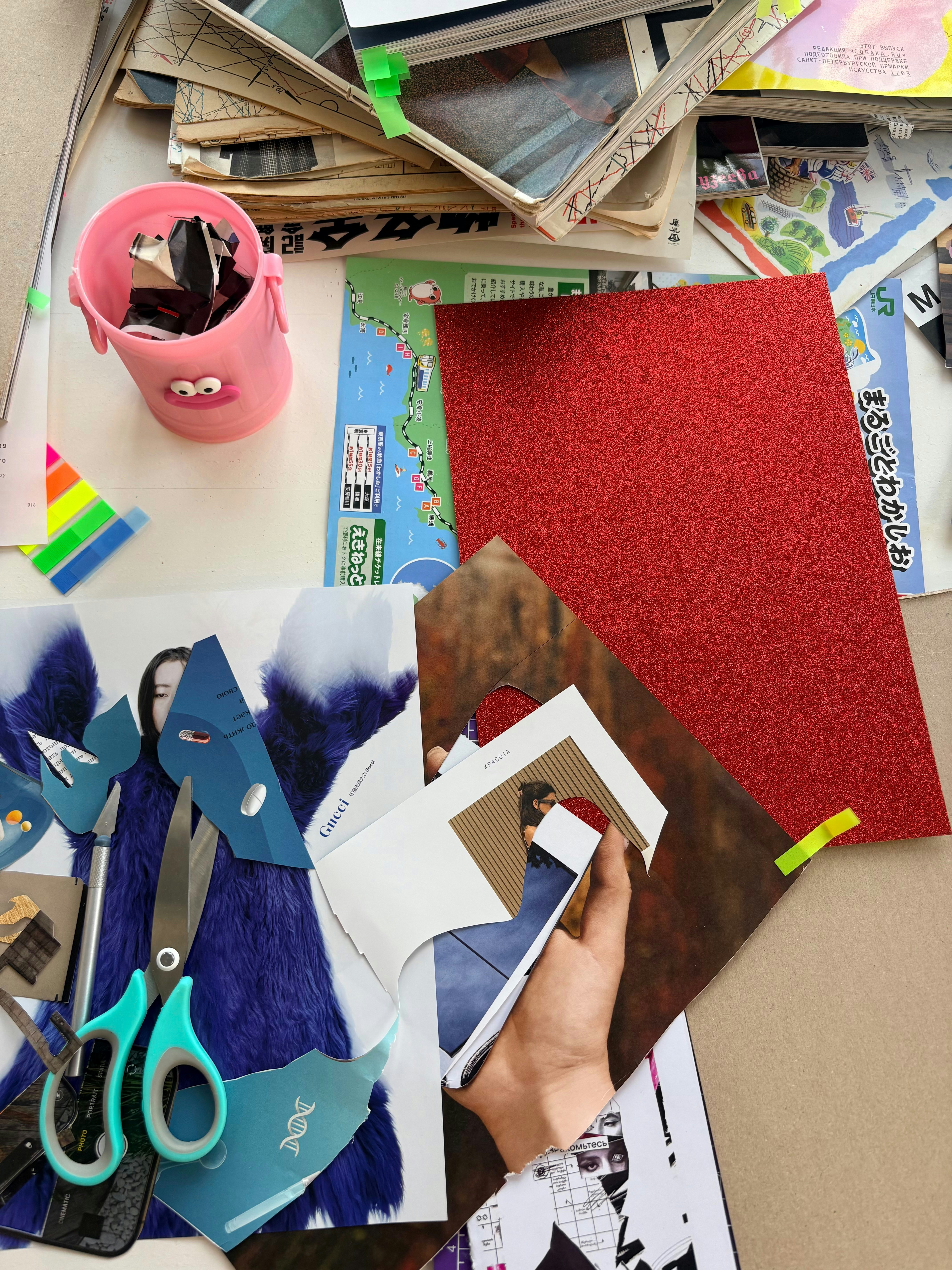 Cluttered desk with crafting supplies, scissors, and paper for collage.