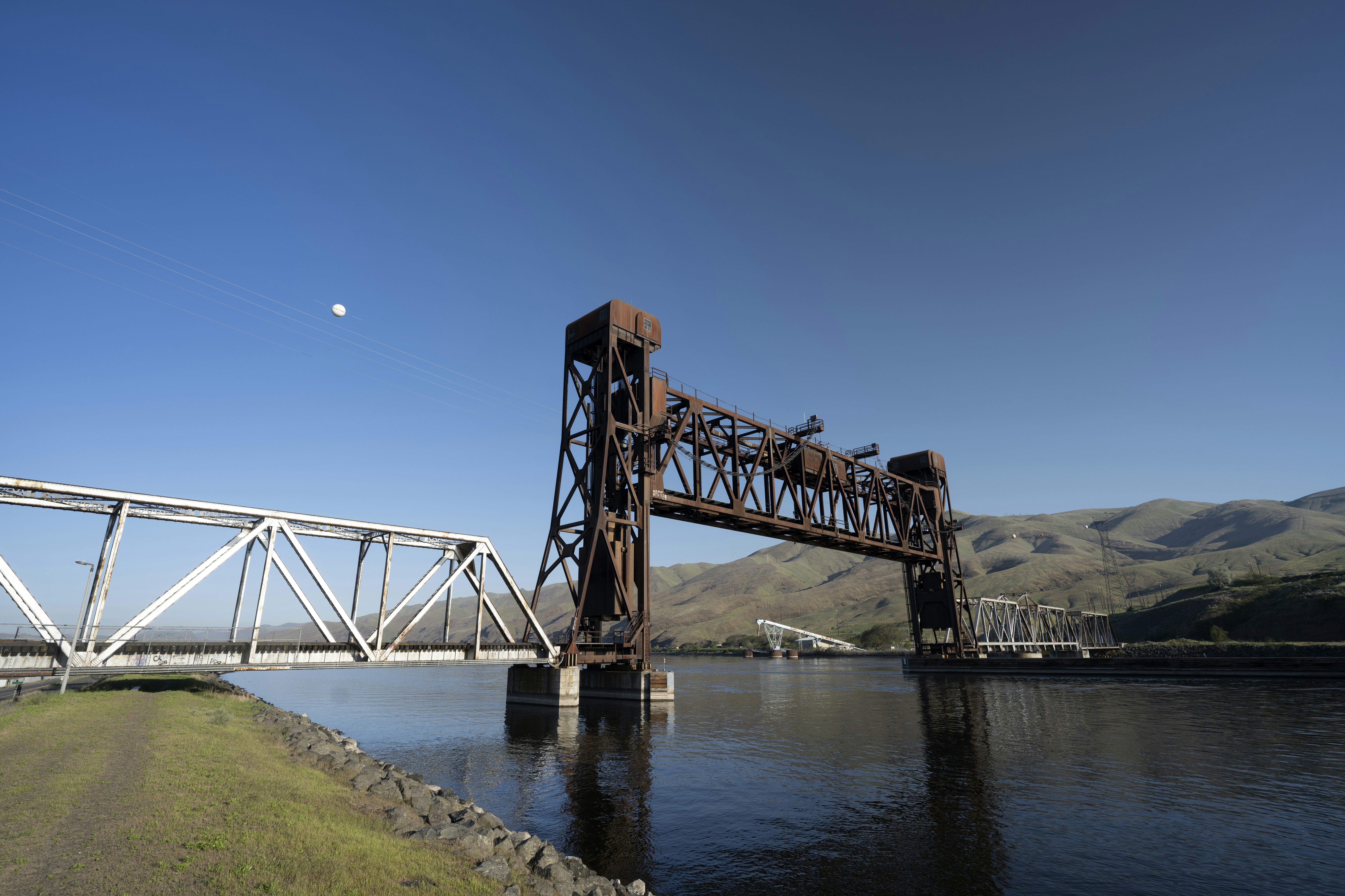 Rust and River: A Railside Gateway under a Clear Sky