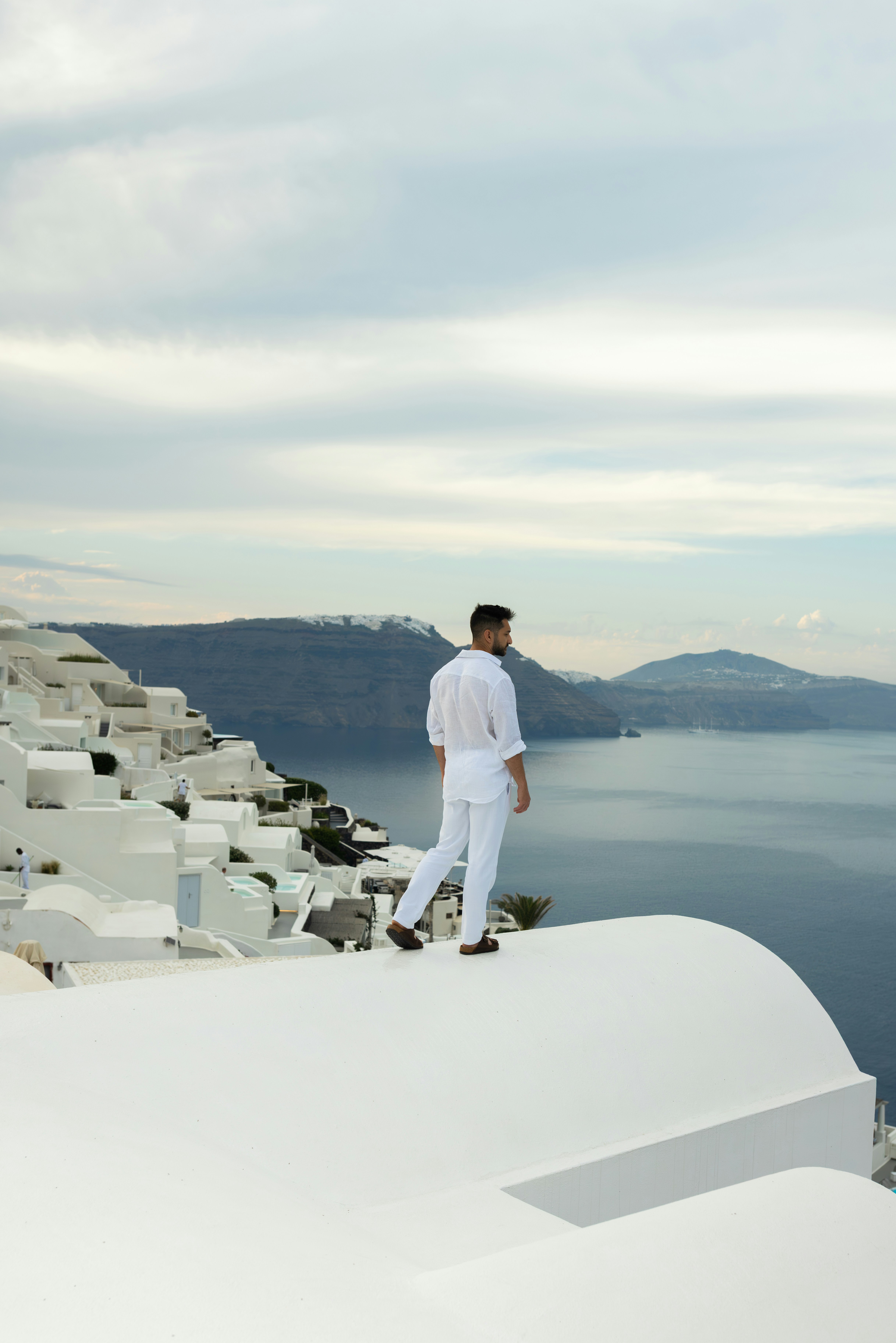 White-clad wanderer atop Santorini's sunlit whitewash, gazing toward the horizon
