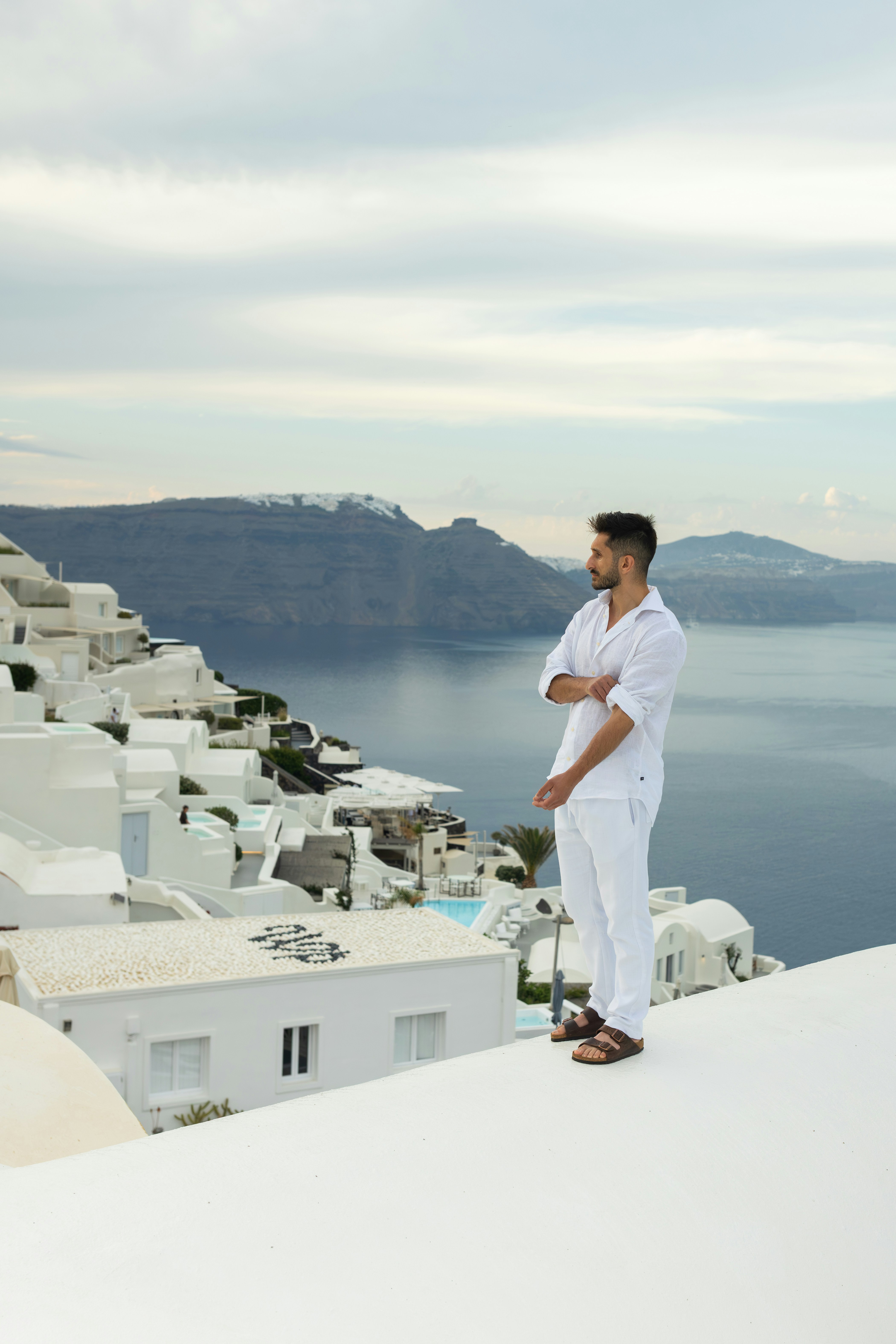 Man in white on a sunlit terrace above the Aegean cliffs