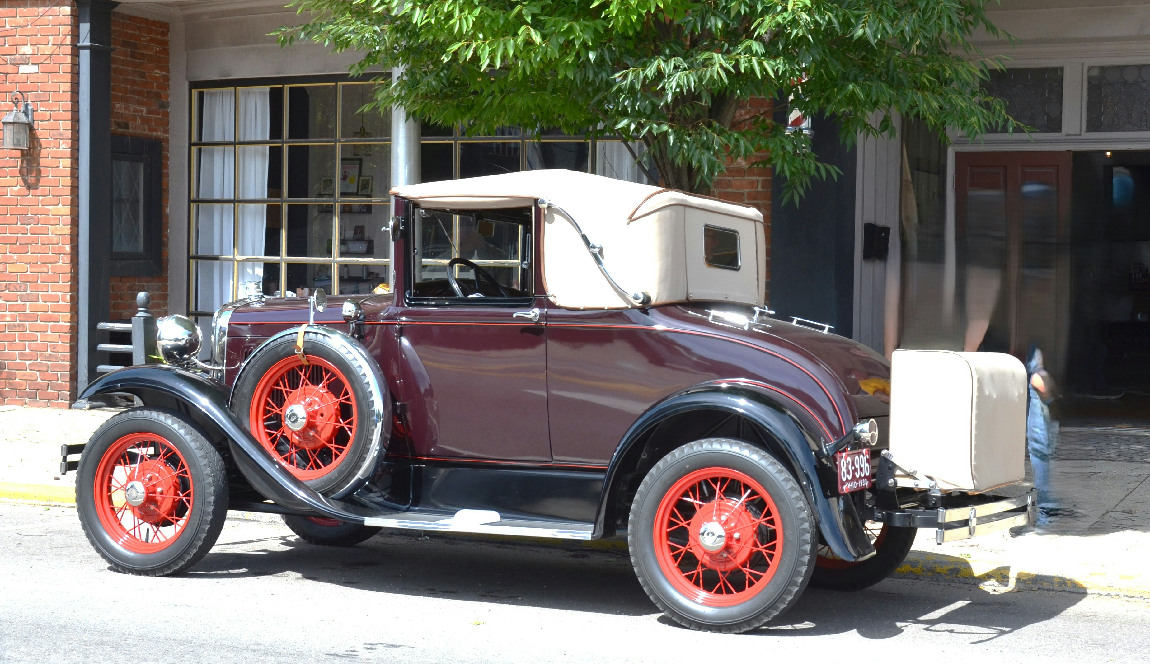 Maroon Classic Convertible with Red Spoked Wheels Under a Shade of Green