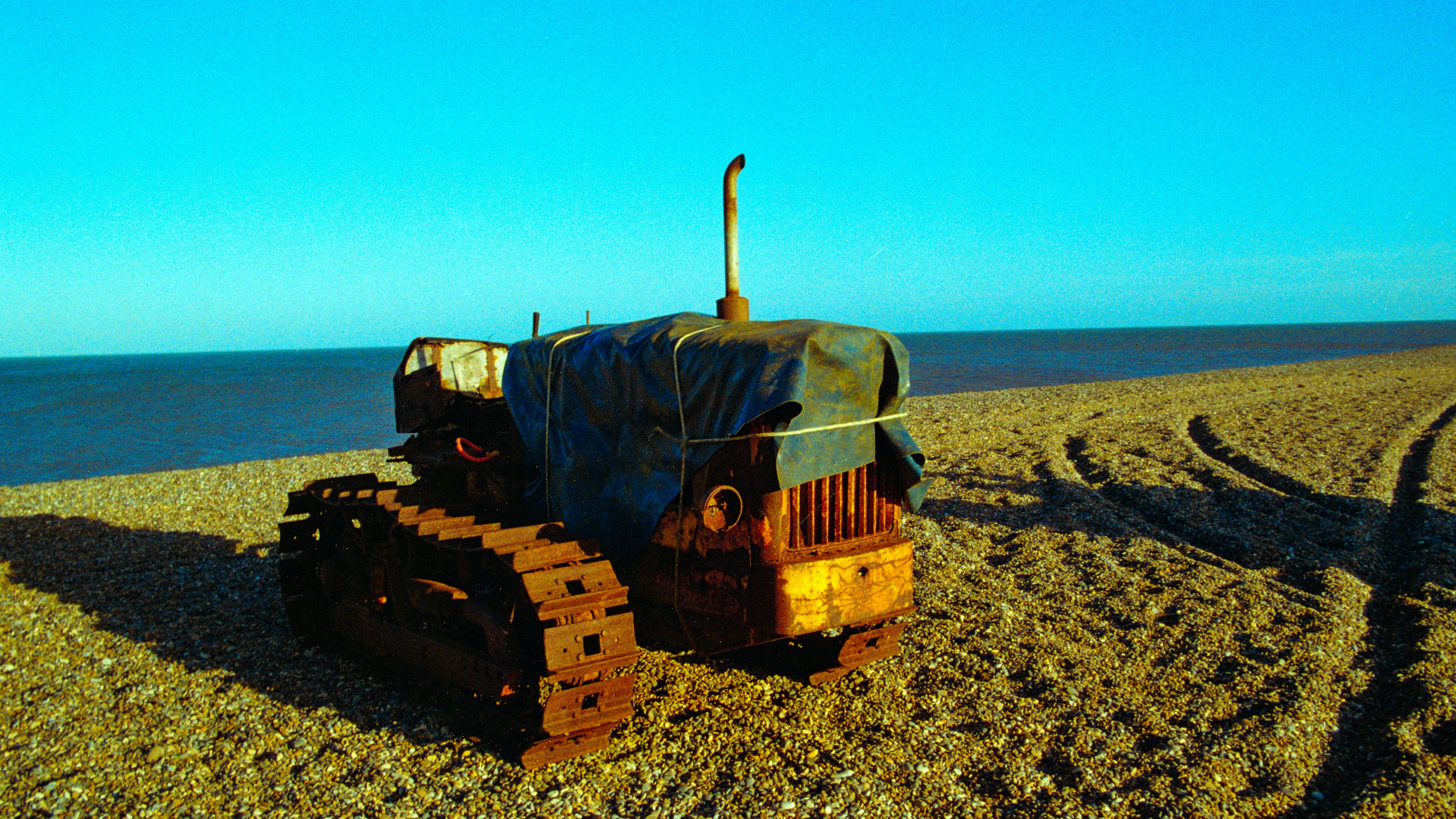 Rusty Track Vehicle Resting on a Pebbled Beach under a Clear Blue Sky