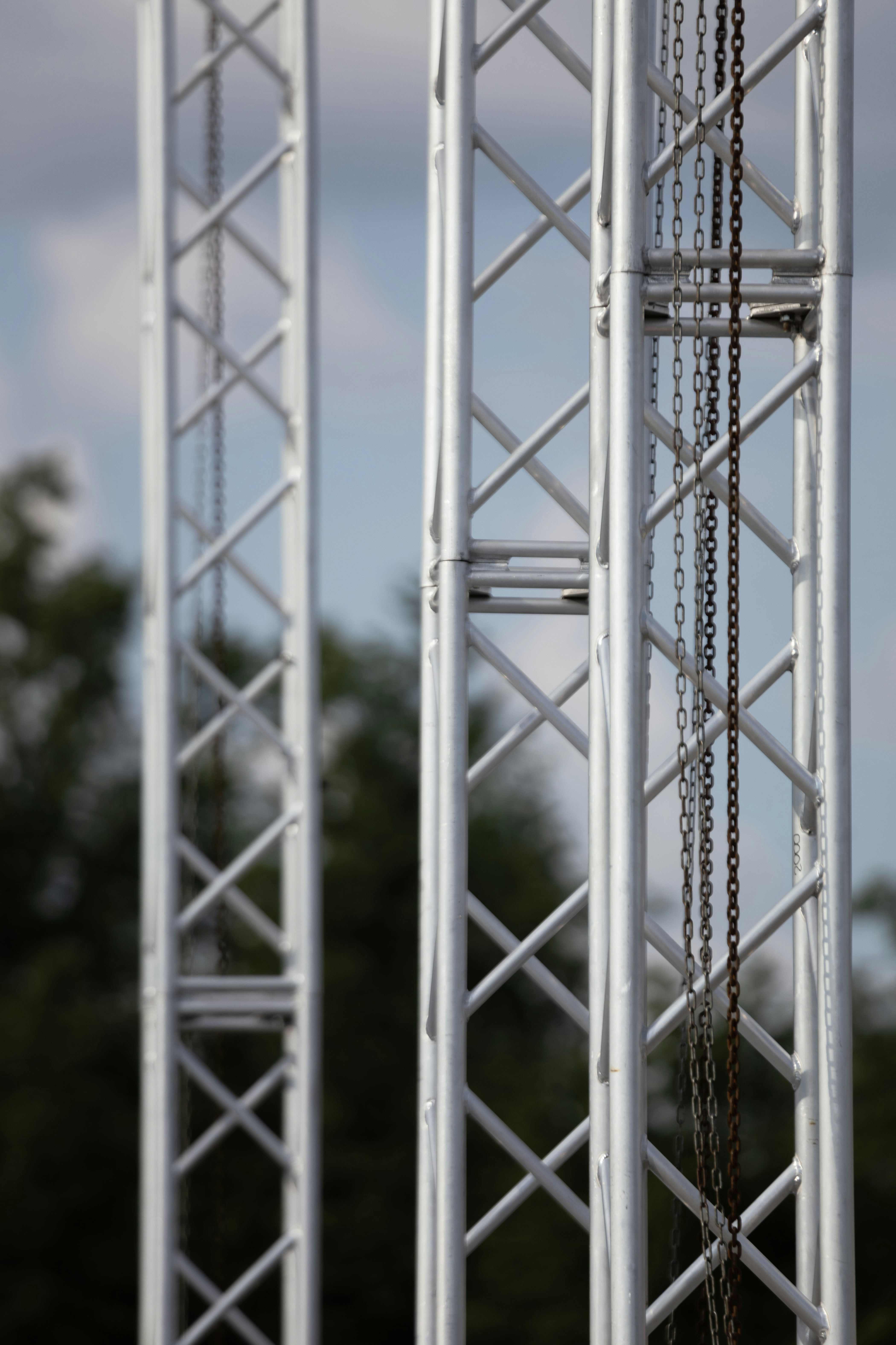 Two white metal trusses with chains against a sky.