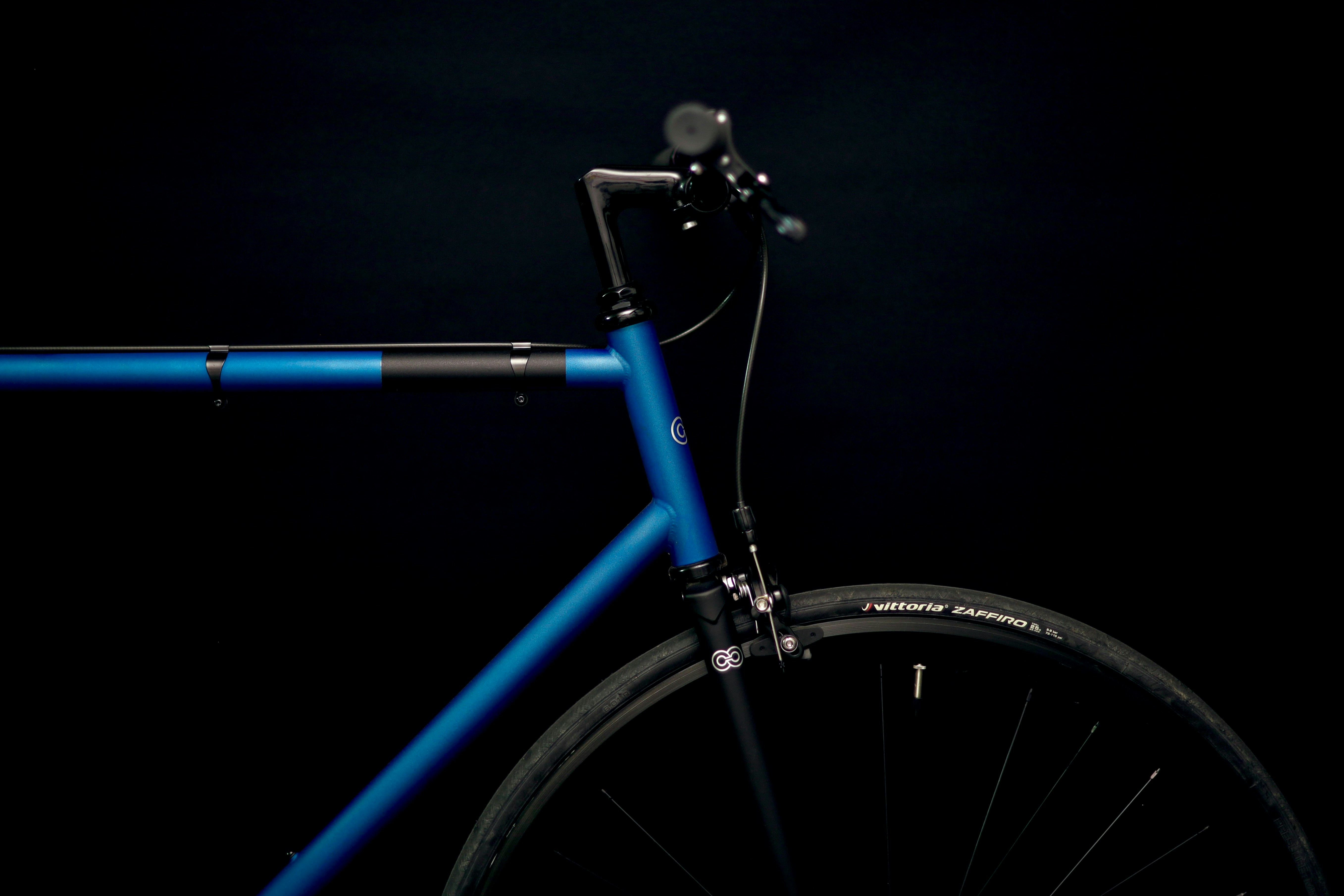 Blue bicycle frame under dark backdrop with front wheel and handlebar in focus