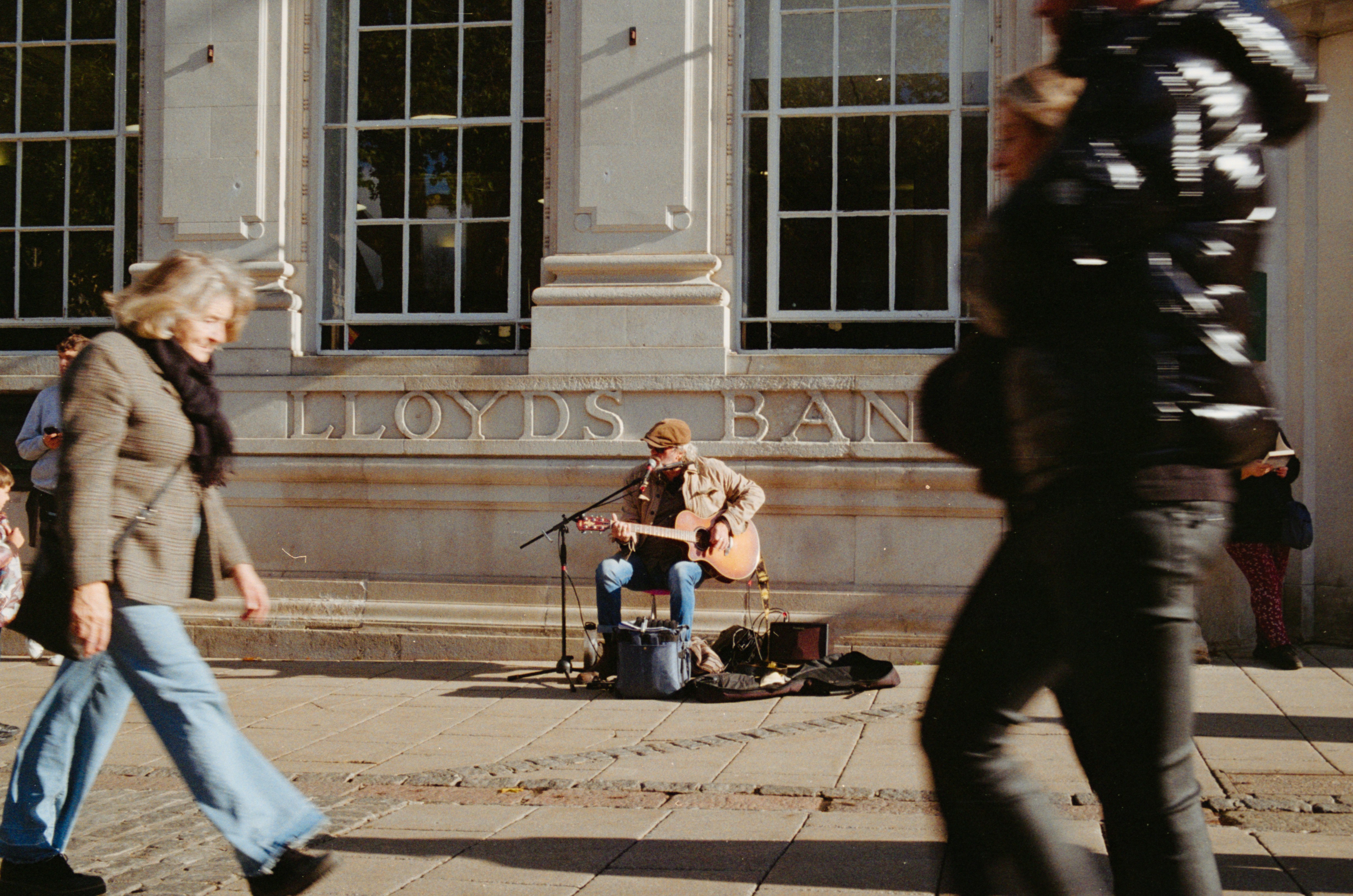 Busker in the shade: a guitarist by the bank façade