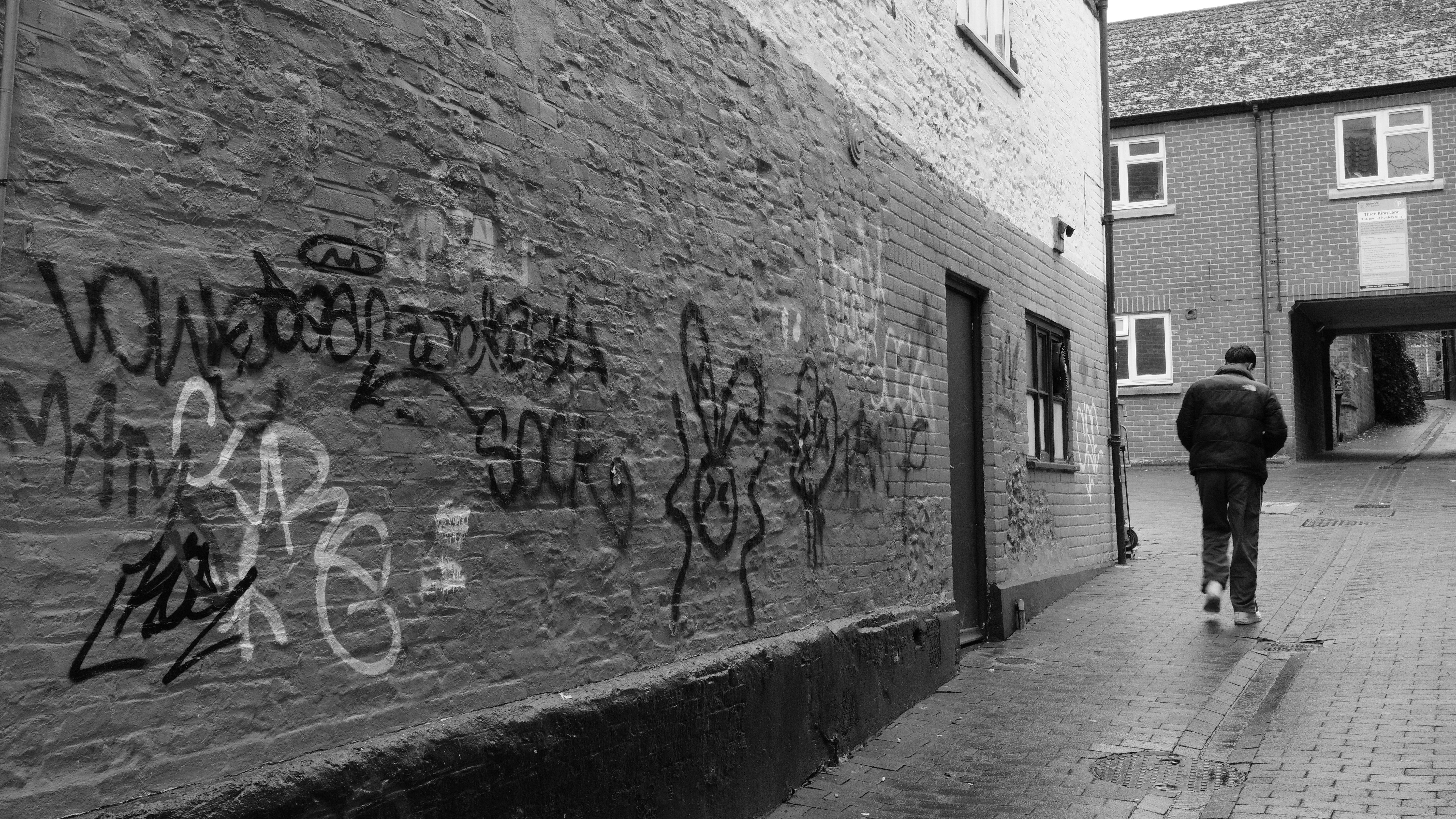 Graffitied Wall, Quiet Escape: A Man Walks Away