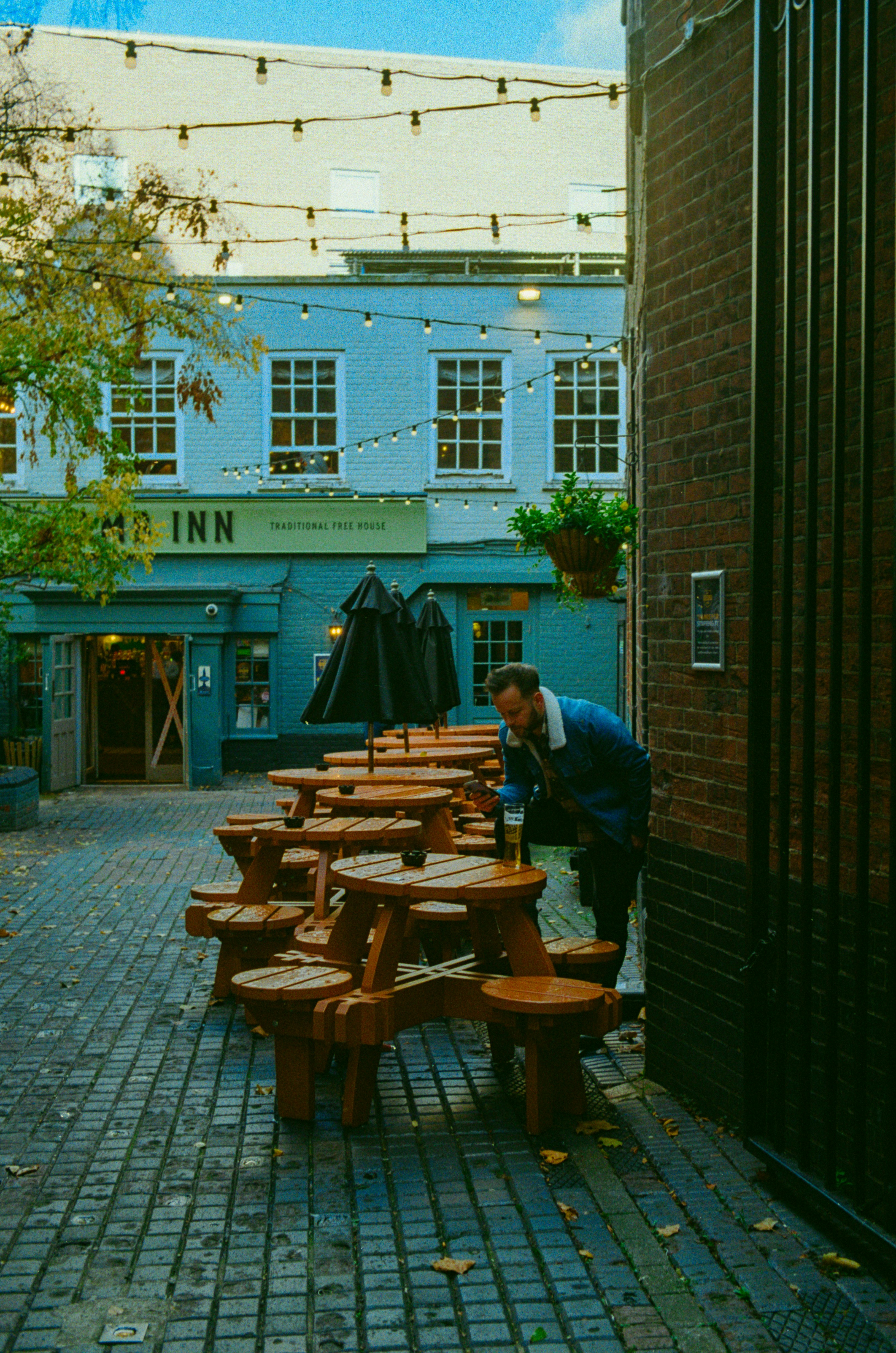 Wooden picnic tables and festoon lights fill a pub courtyard at autumn dusk.