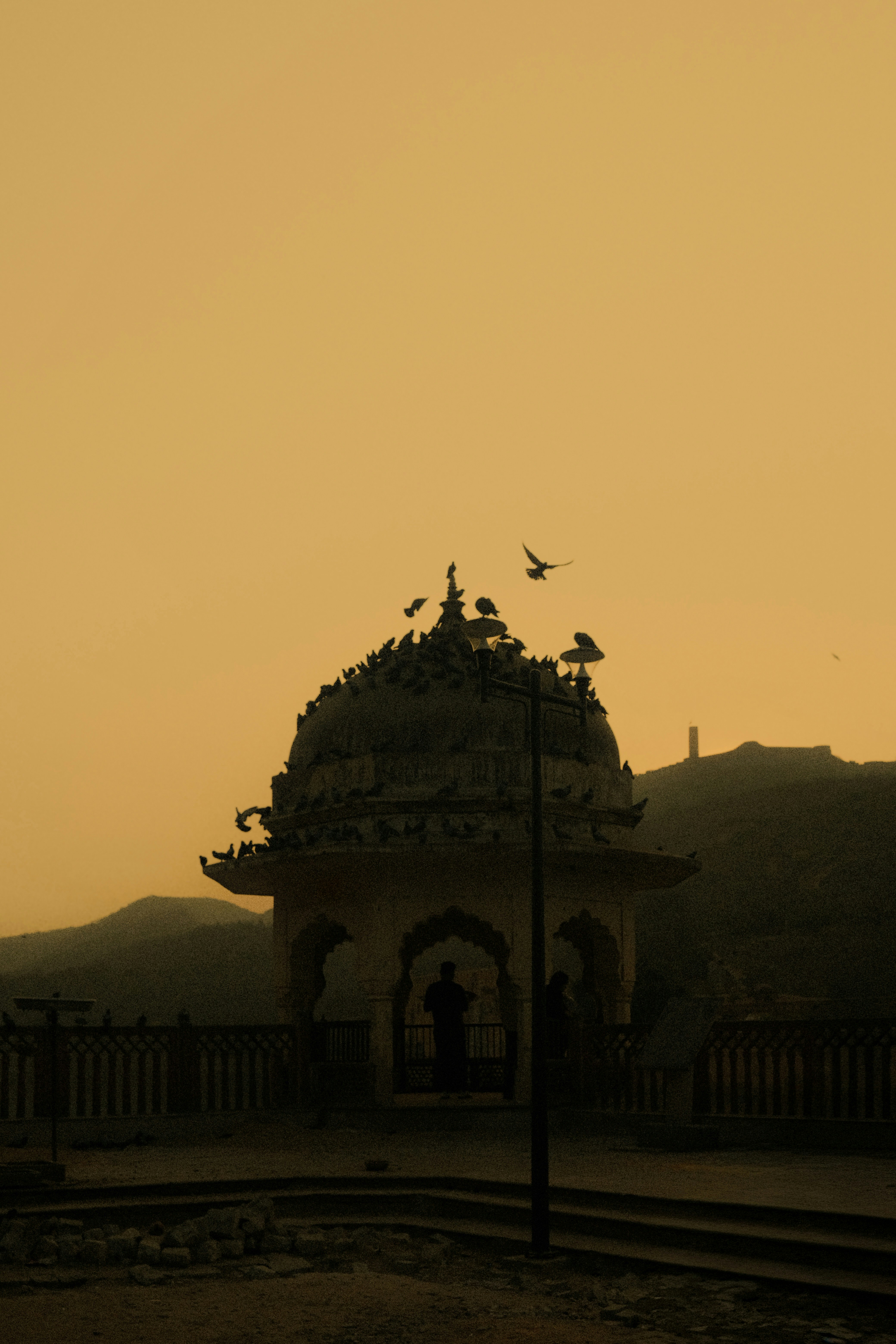 Silhouetted dome with birds and person against an orange sky.