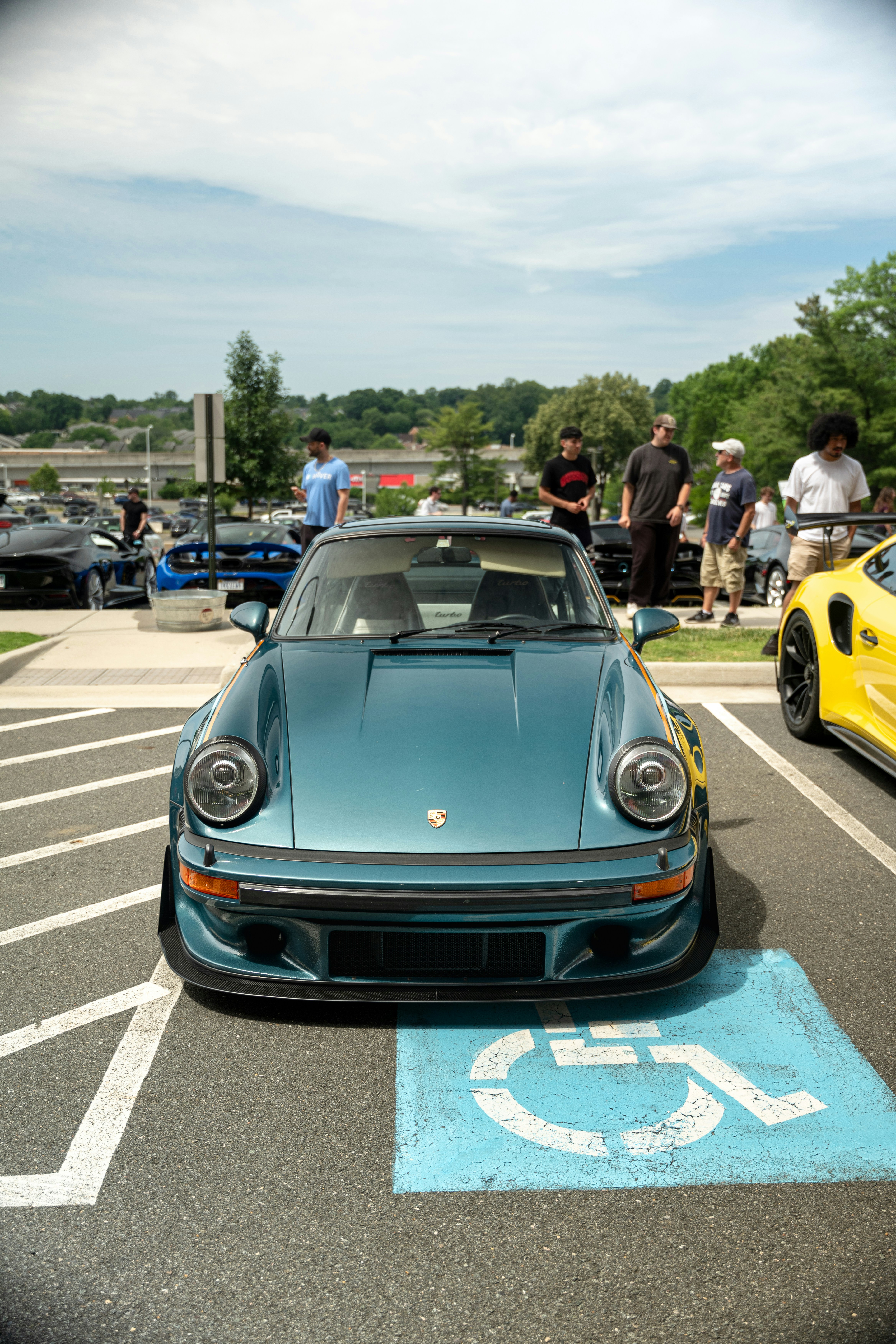 A teal porsche car parked in a handicapped parking spot.