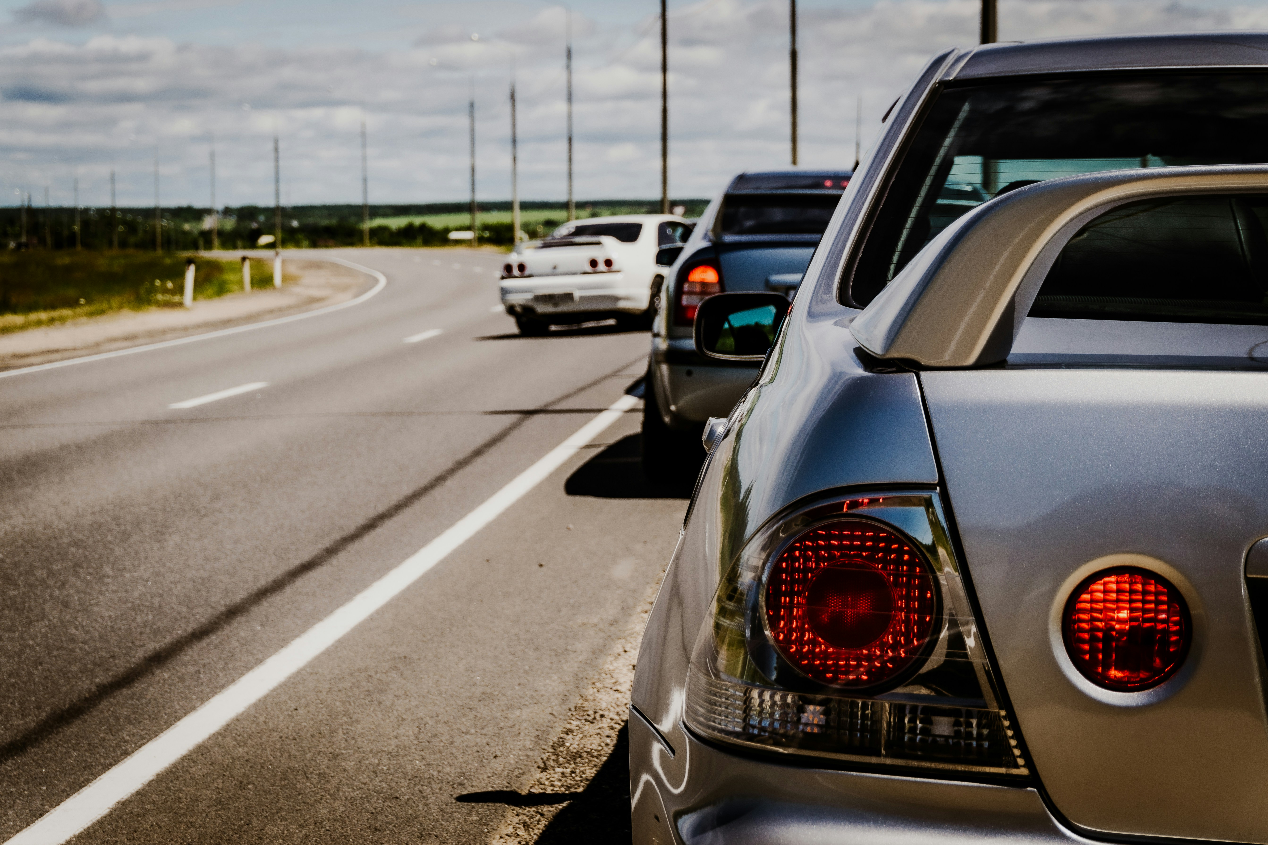 Tail lights on the highway: a chrome sedan leads the line