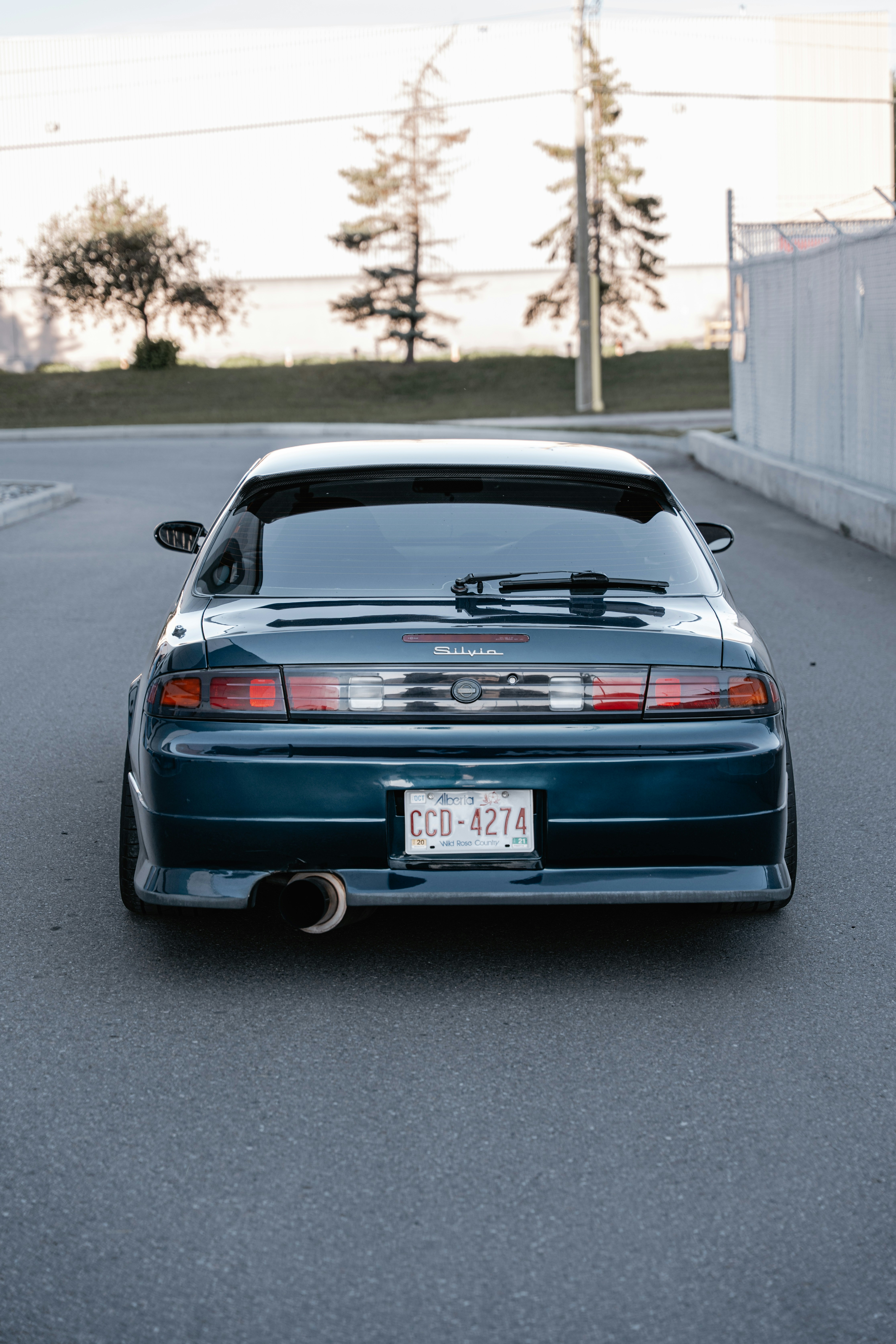 Dark teal car parked on asphalt with trees in background.