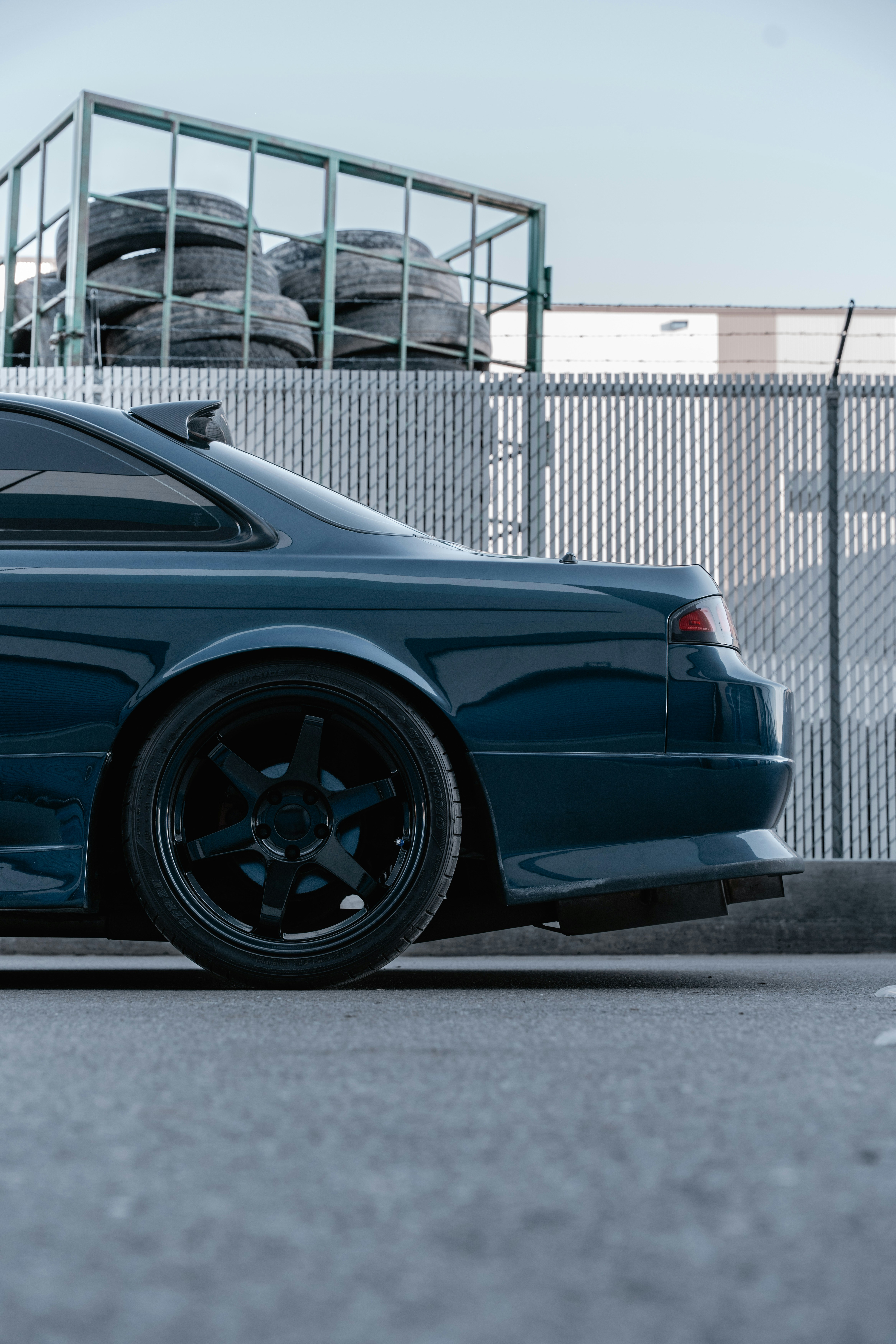 Low-Angle Shadowed Stance: A Dark Blue Coupe by the Fence