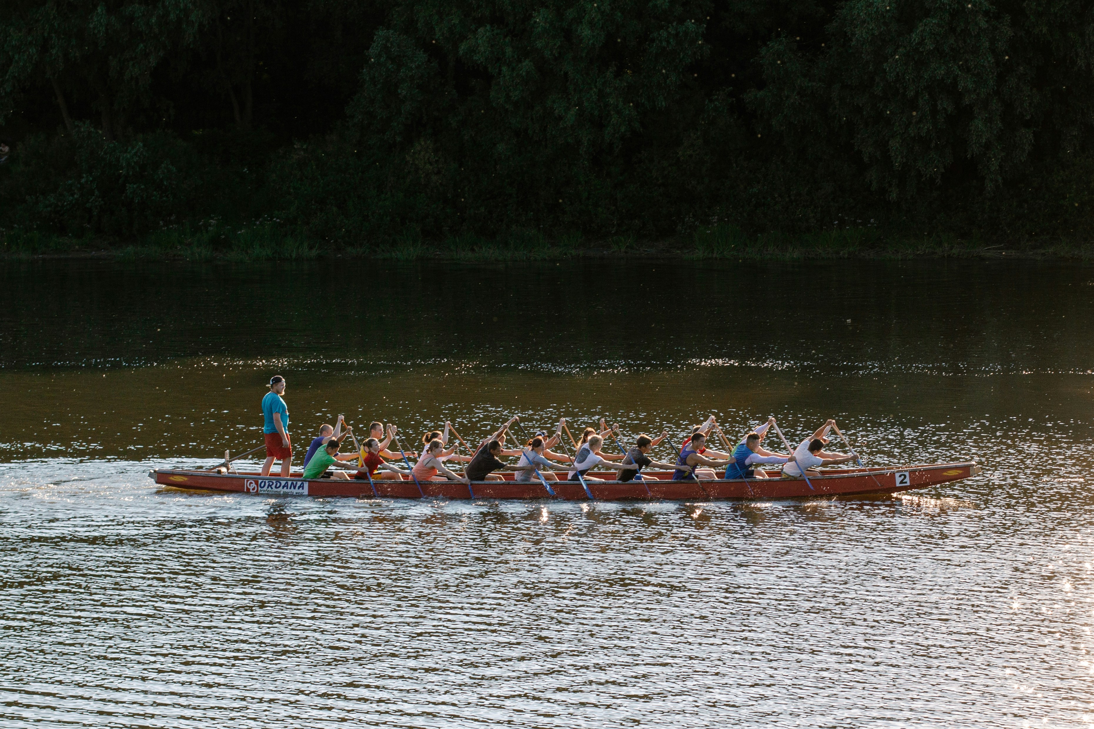 Team in a Long Boat Slicing Through Glassy River Light