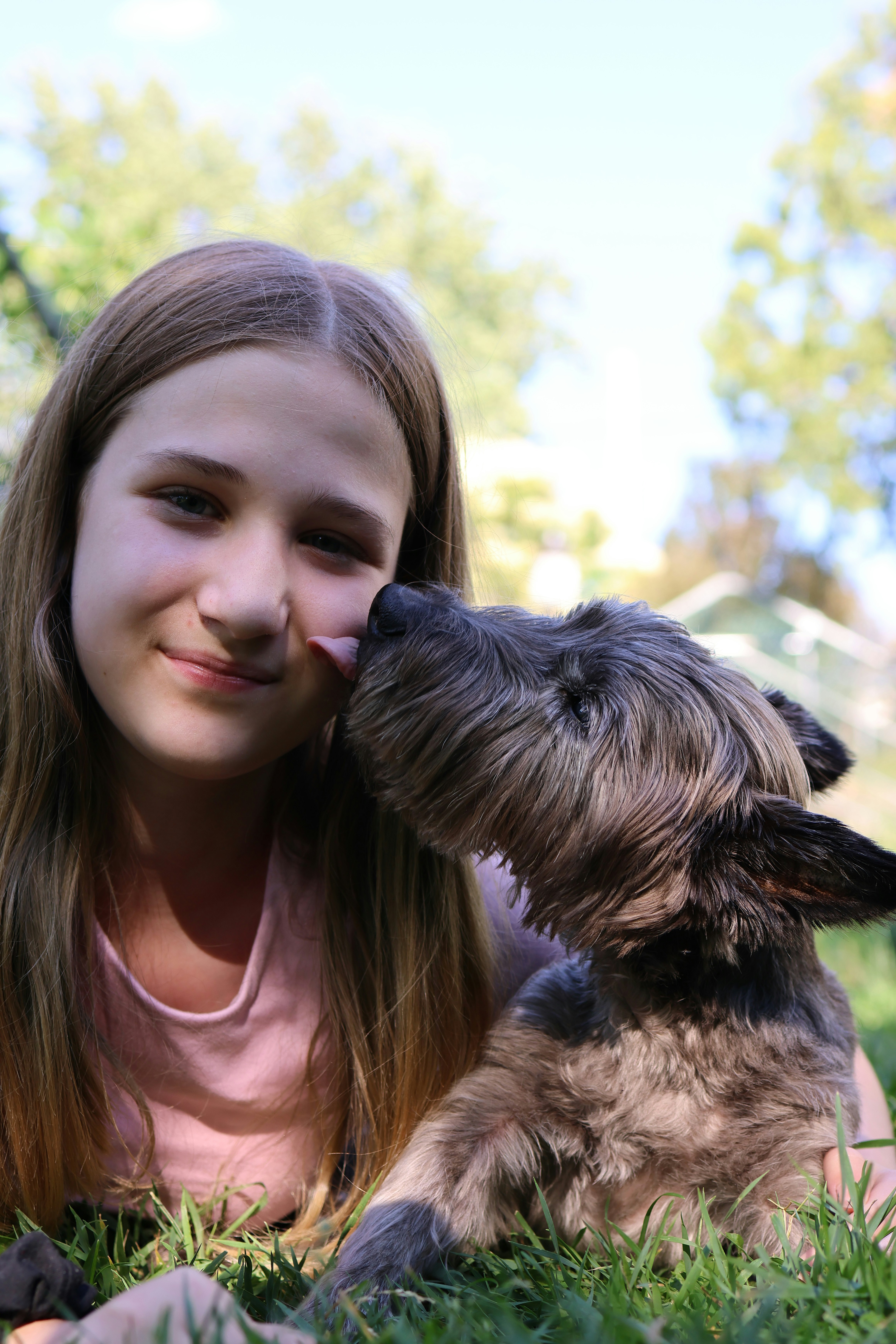 Loyalty in Light: Girl and Dog Share a Quiet Kiss in the Sunlit Yard