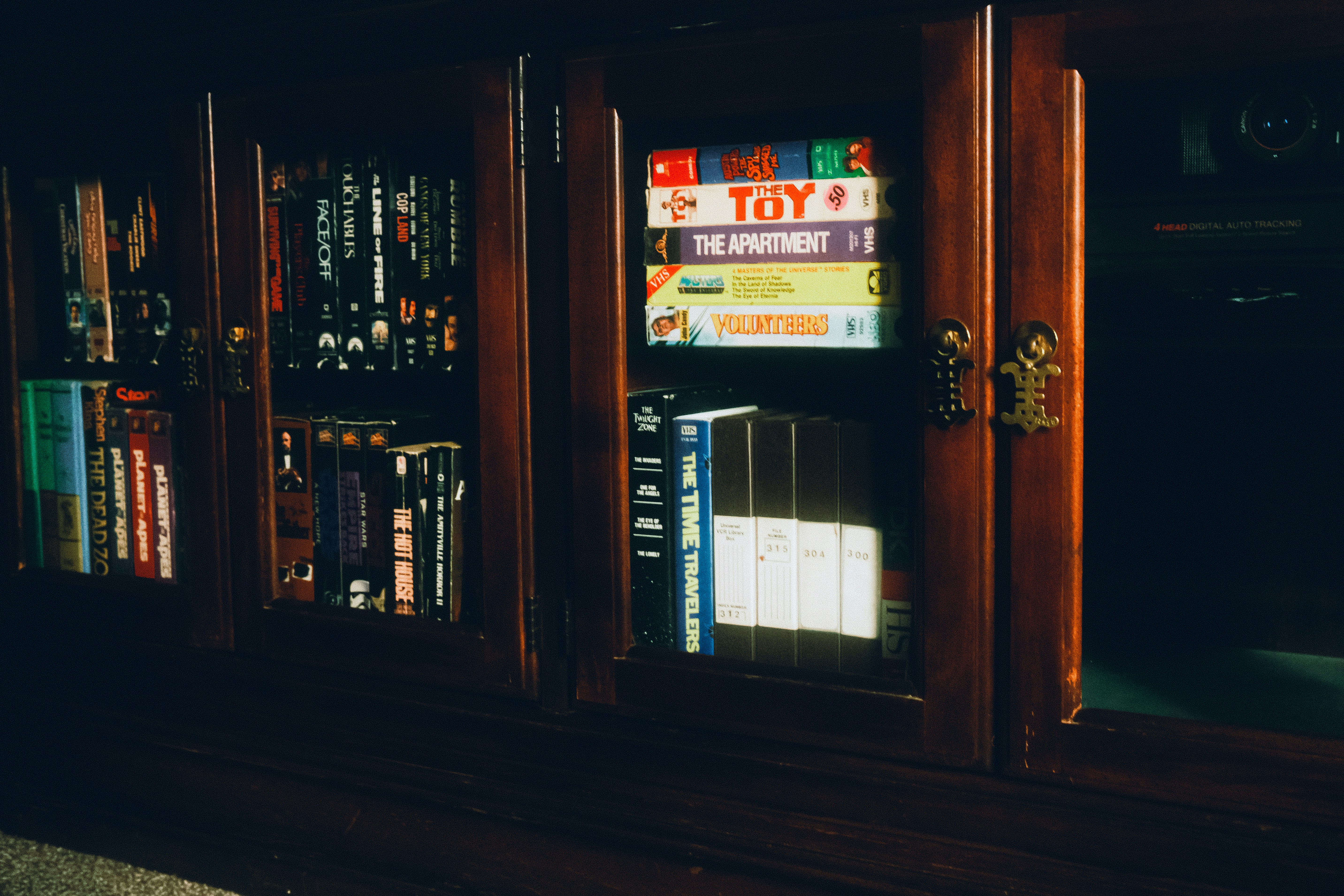 A wooden cabinet filled with books and vintage vhs tapes.