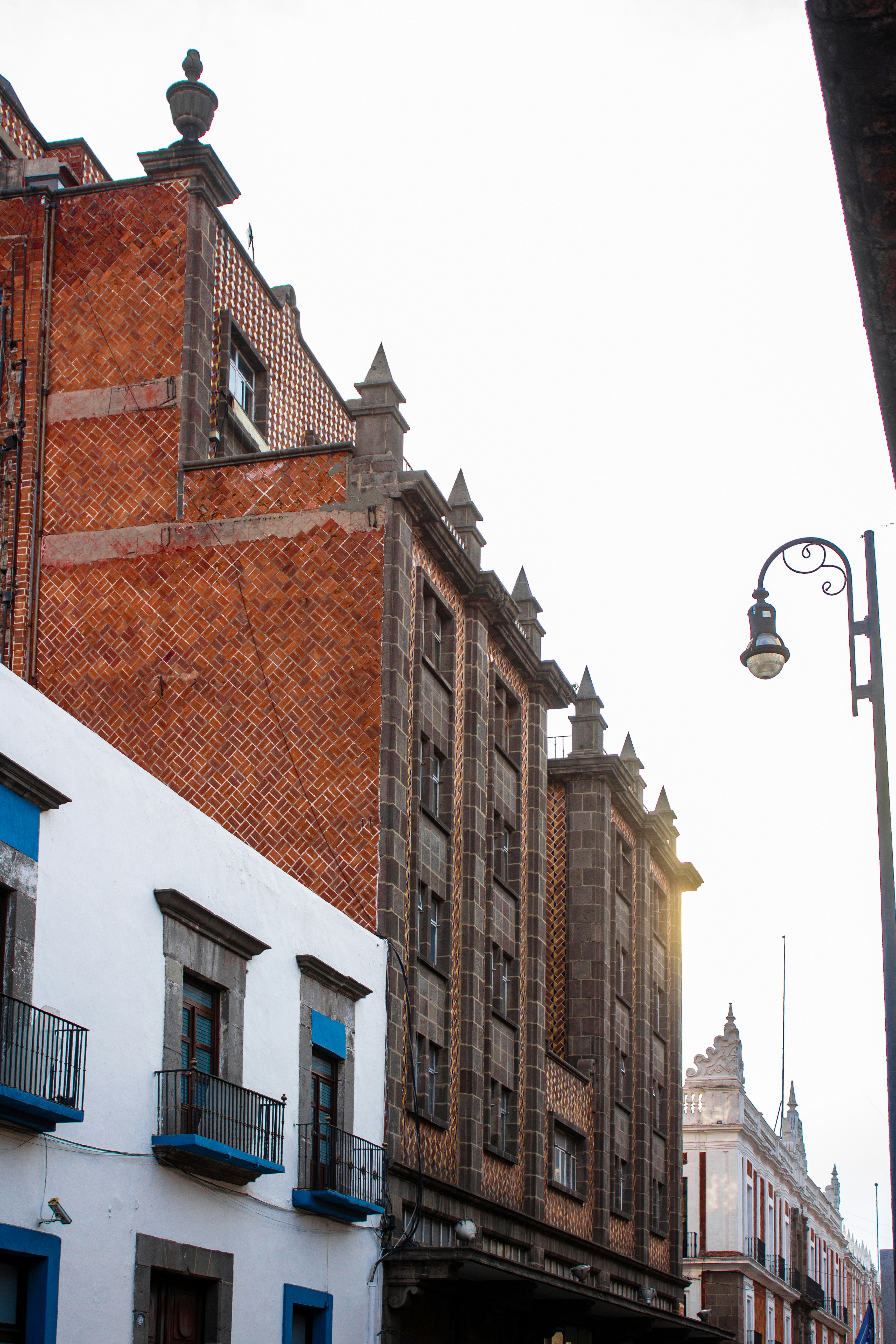 Morning light spills along a row of brick and stucco buildings, with a decorative street lamp and distant tower silhouette.