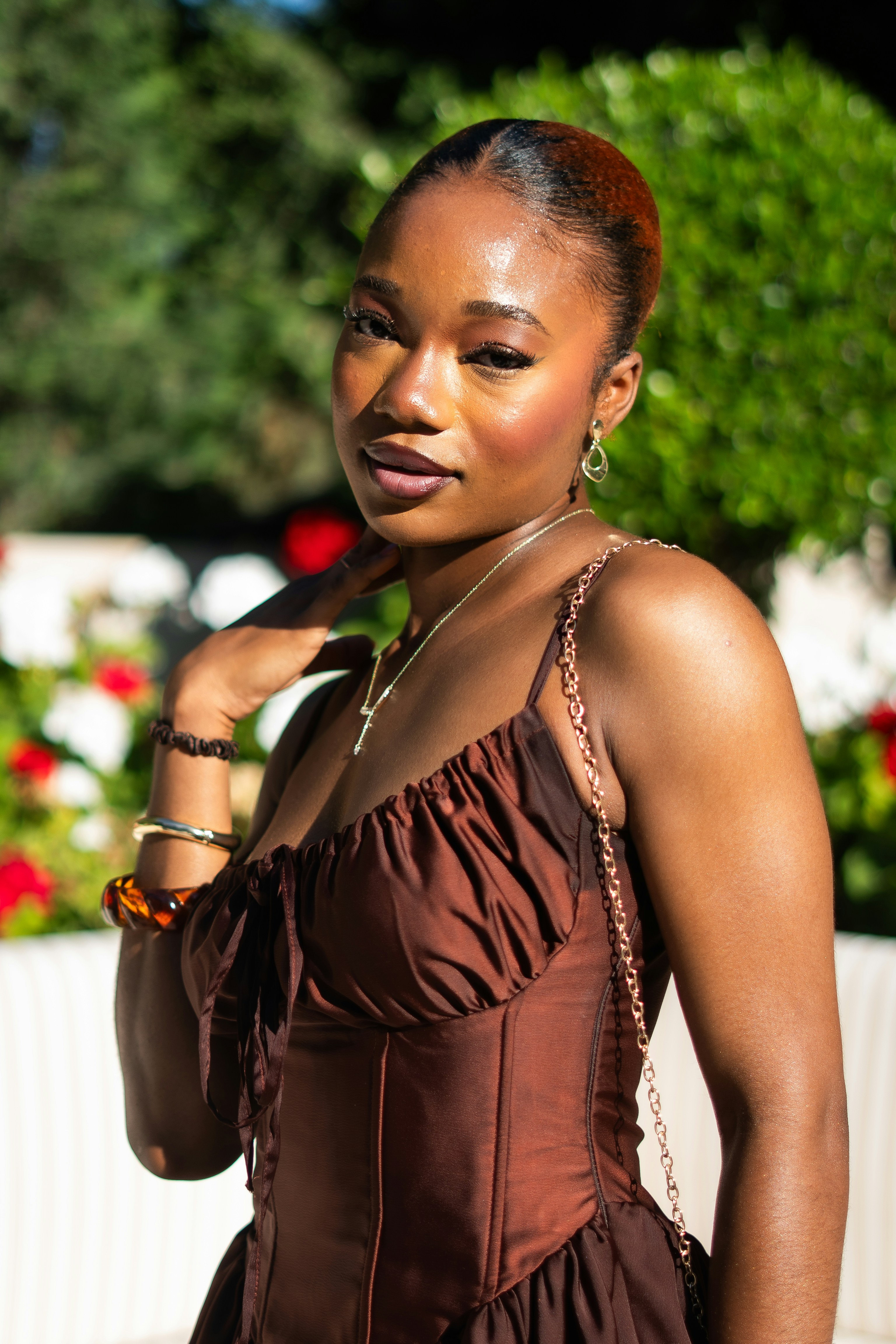 A young woman in a brown dress poses outdoors.