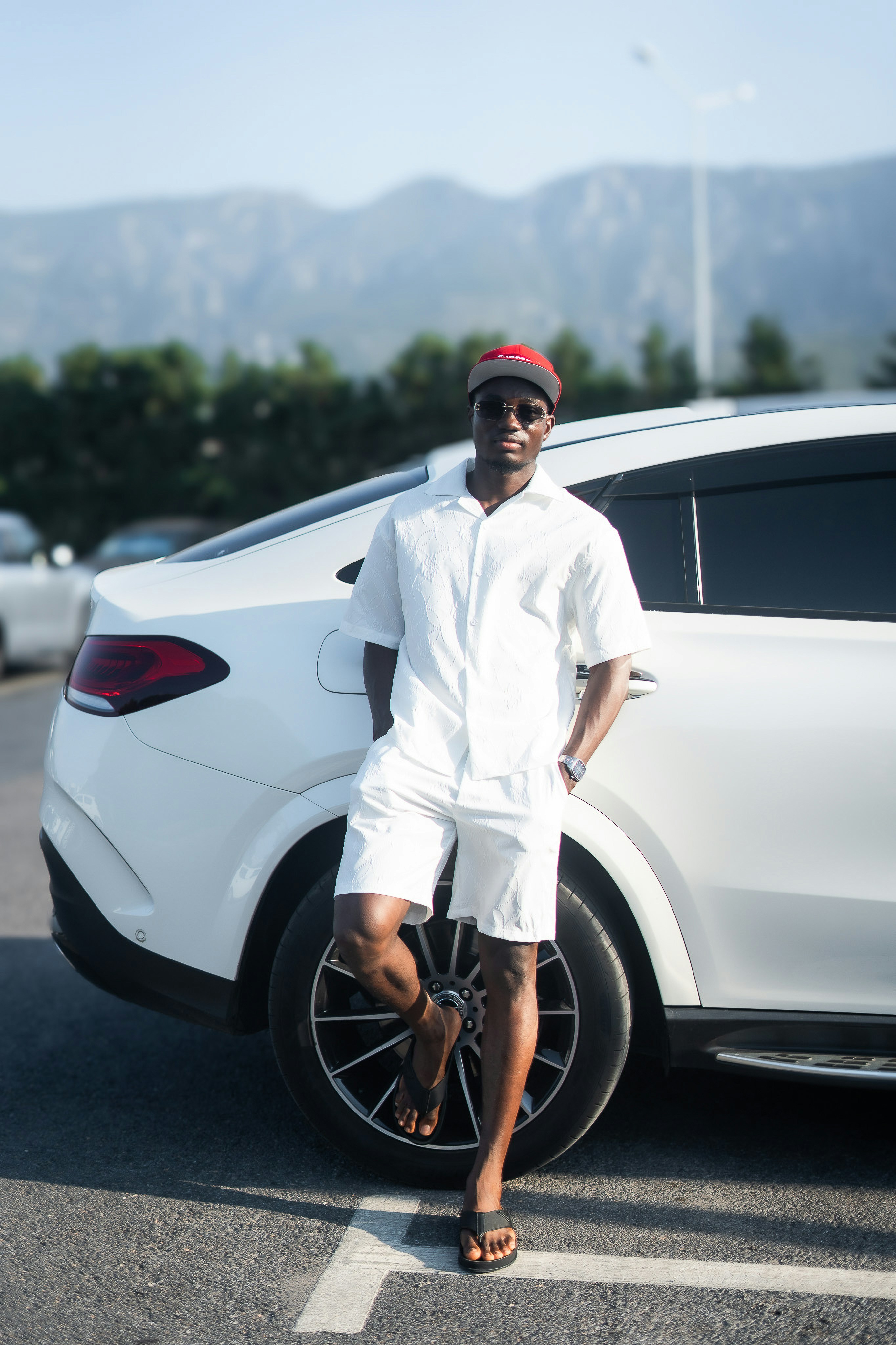 White-silver stance: man in white outfit beside a luxury SUV under a mountain backdrop