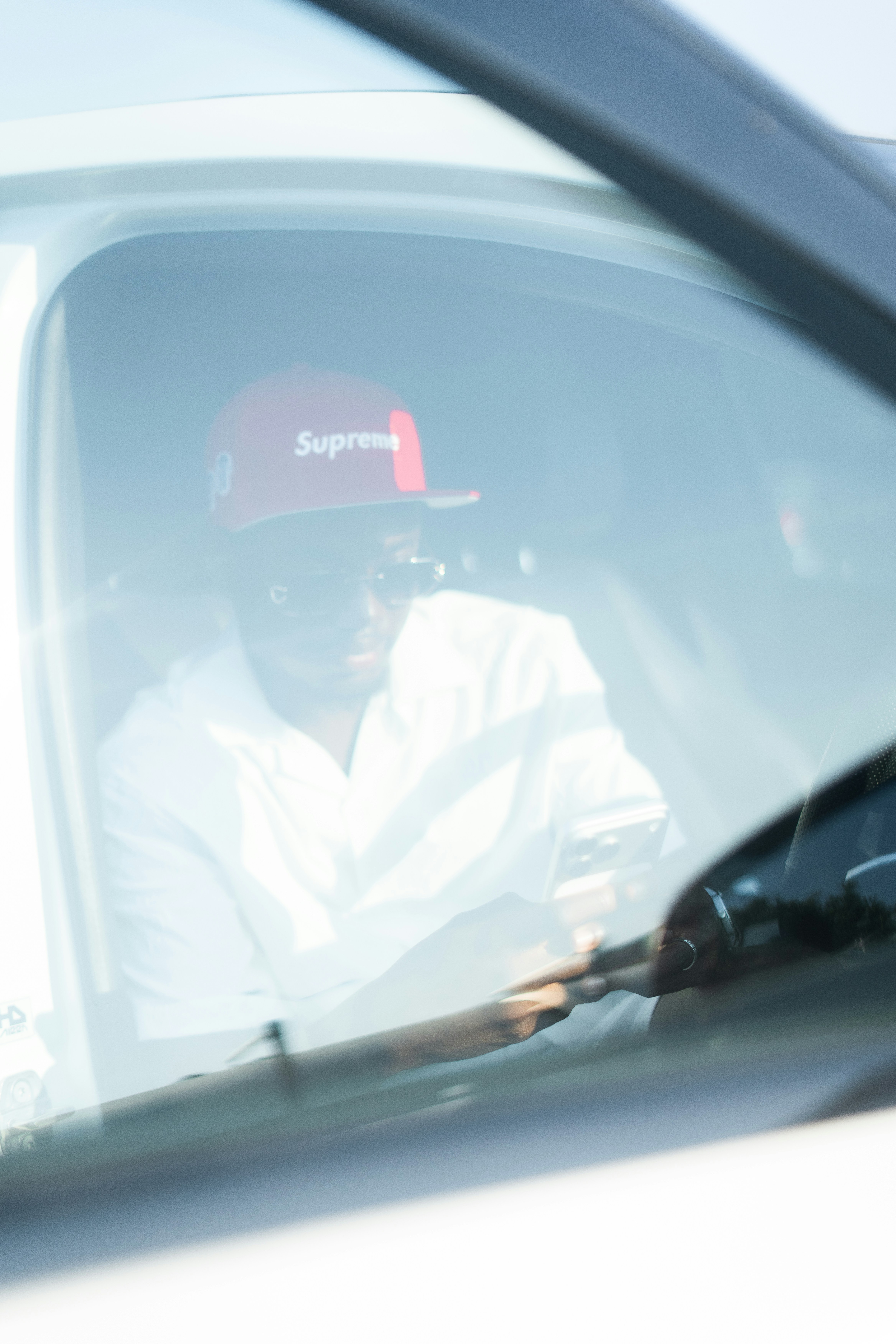 Man wearing red supreme cap and sunglasses driving car.