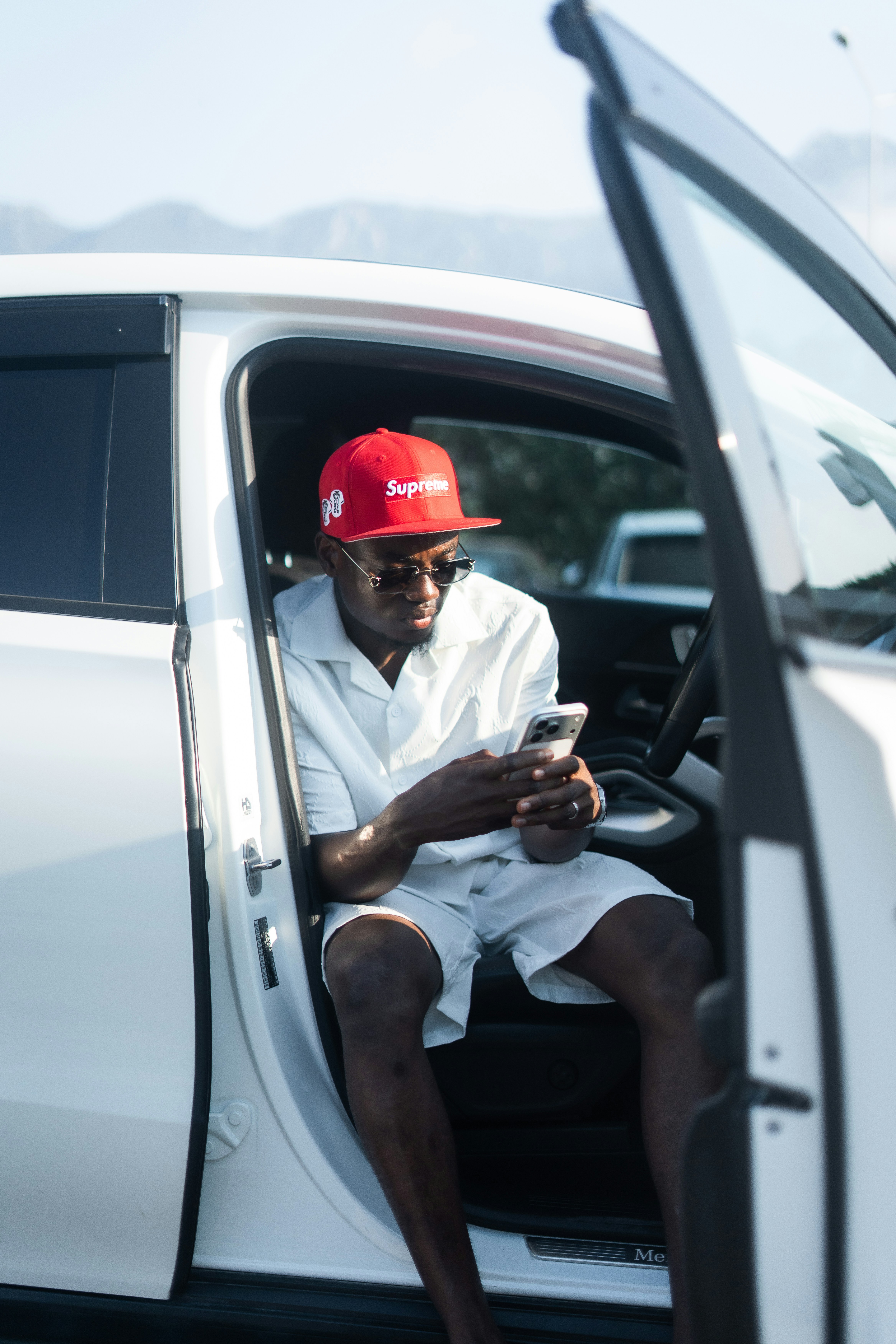 Man in red hat and sunglasses using phone in car.