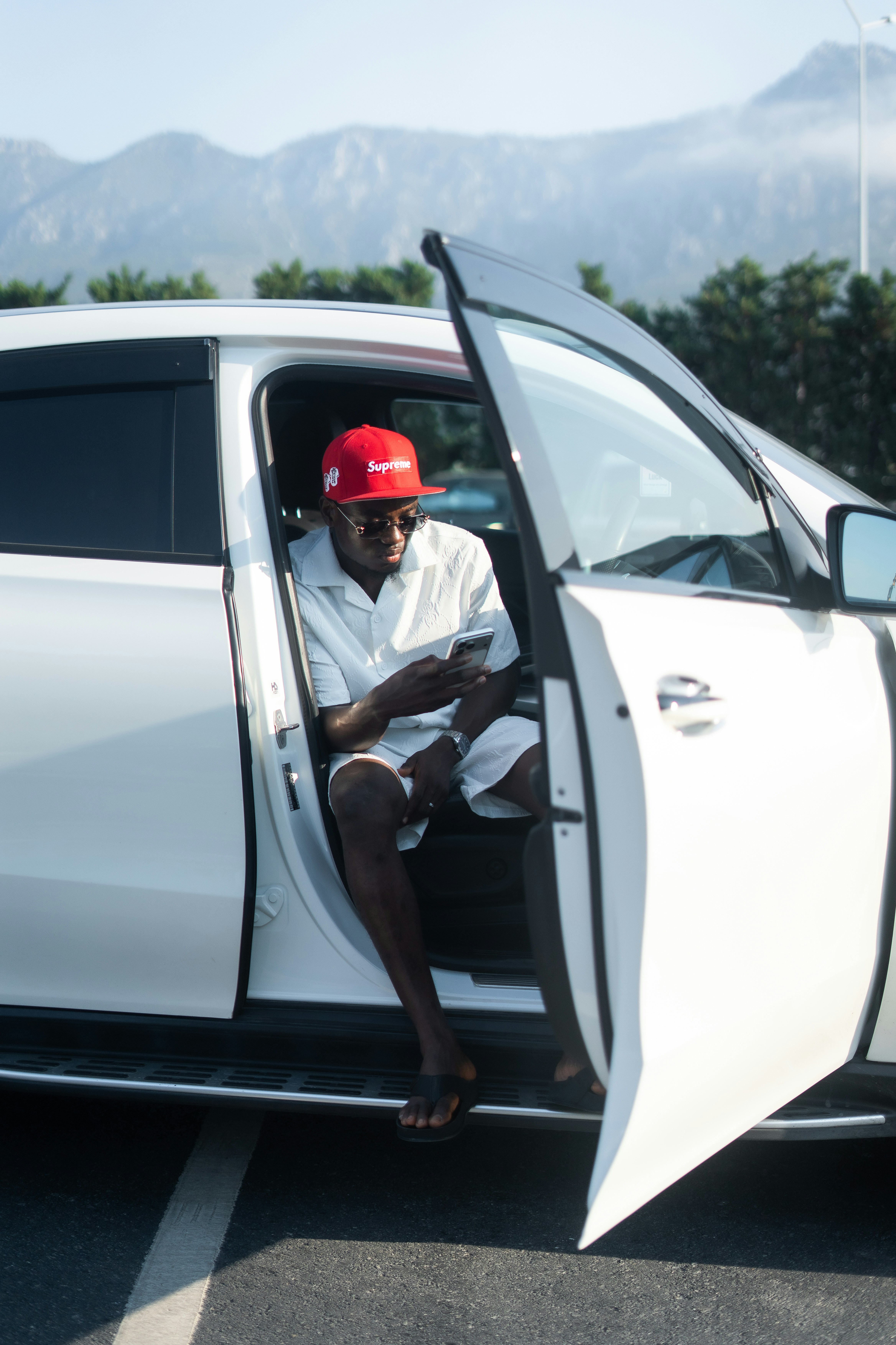 Man in red cap uses phone in white car.