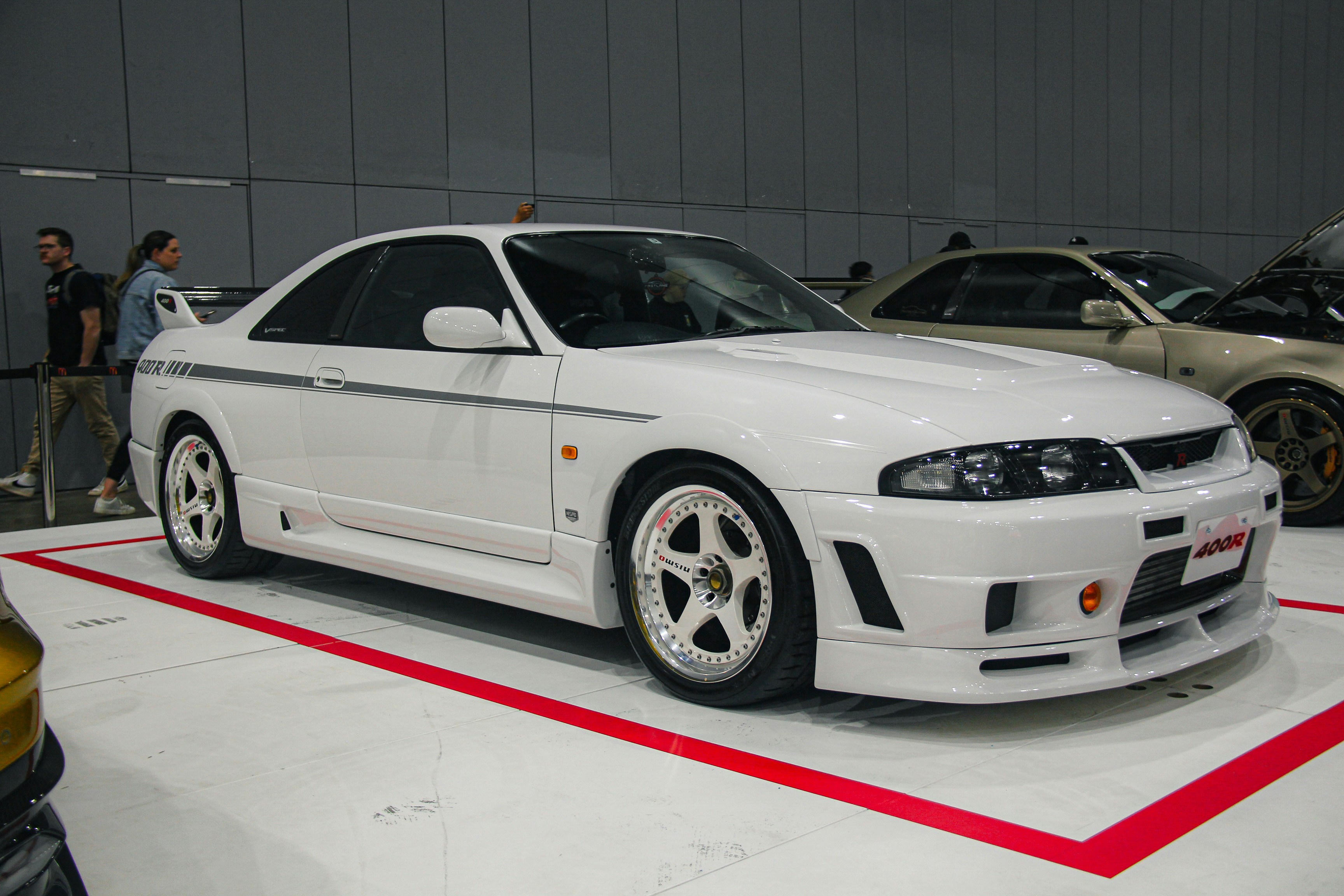 White sport coupe at a car show, low-angle stance emphasizes aerodynamic lines