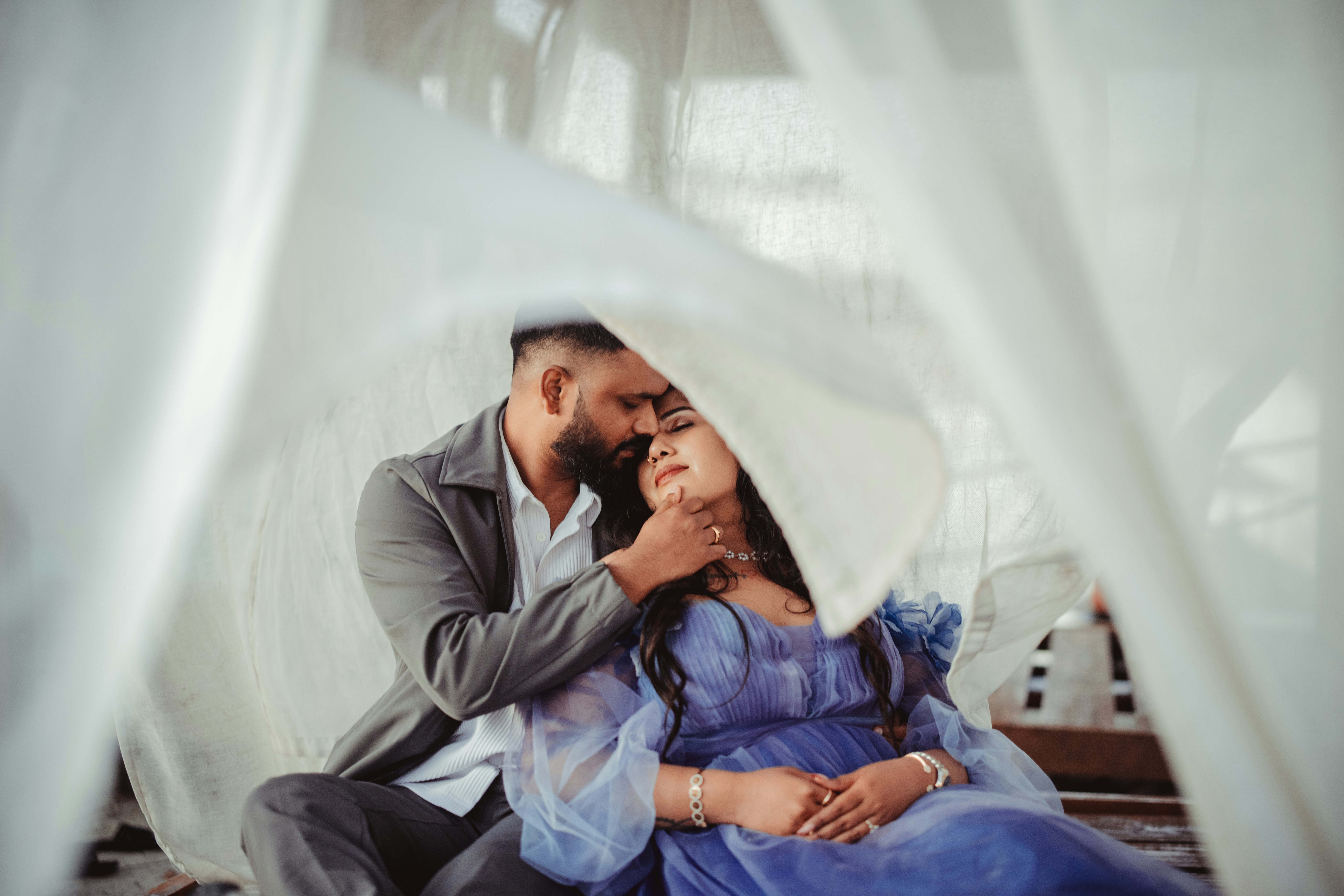 Couple embracing behind sheer white curtains.