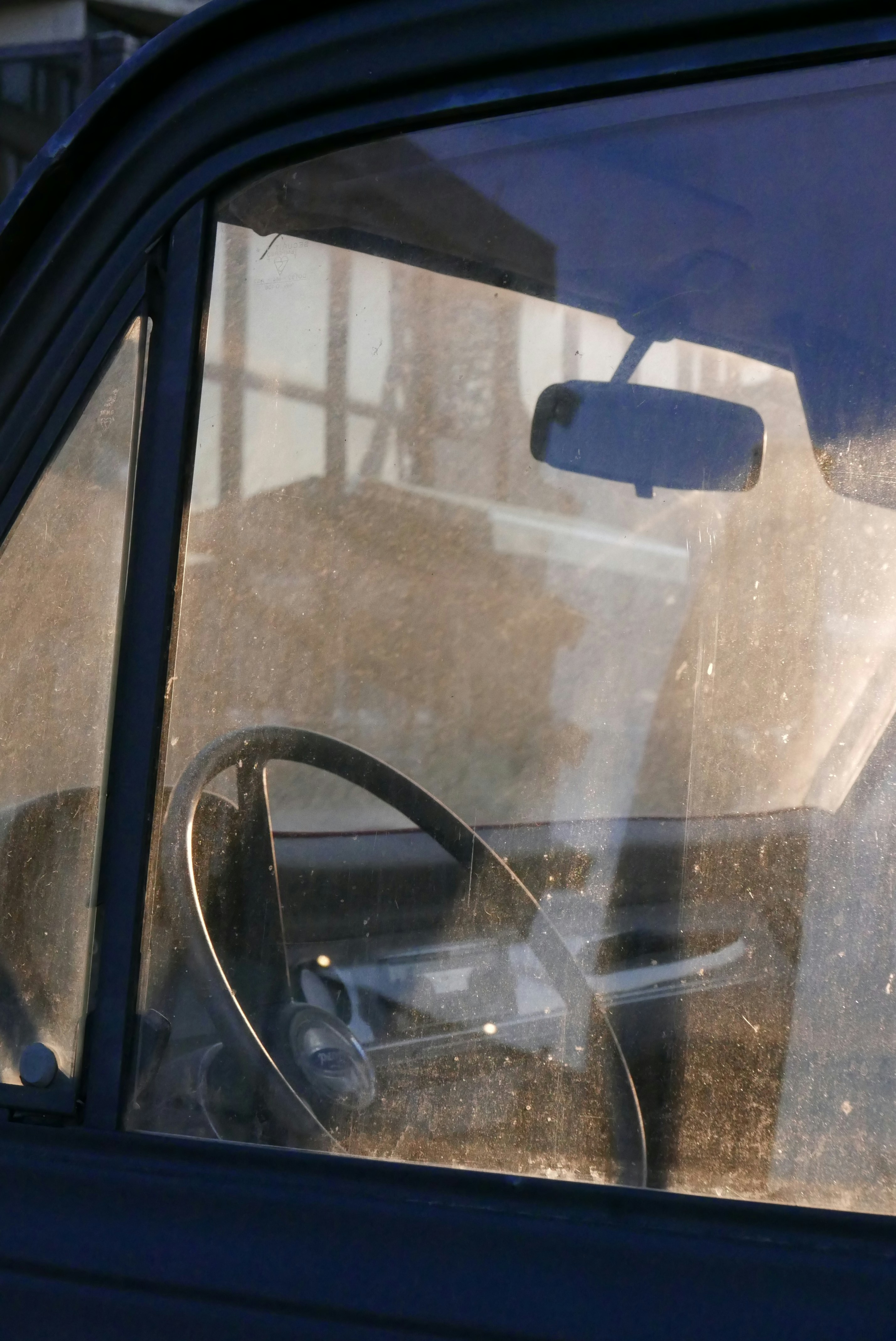 Dusty car interior with steering wheel and rearview mirror.