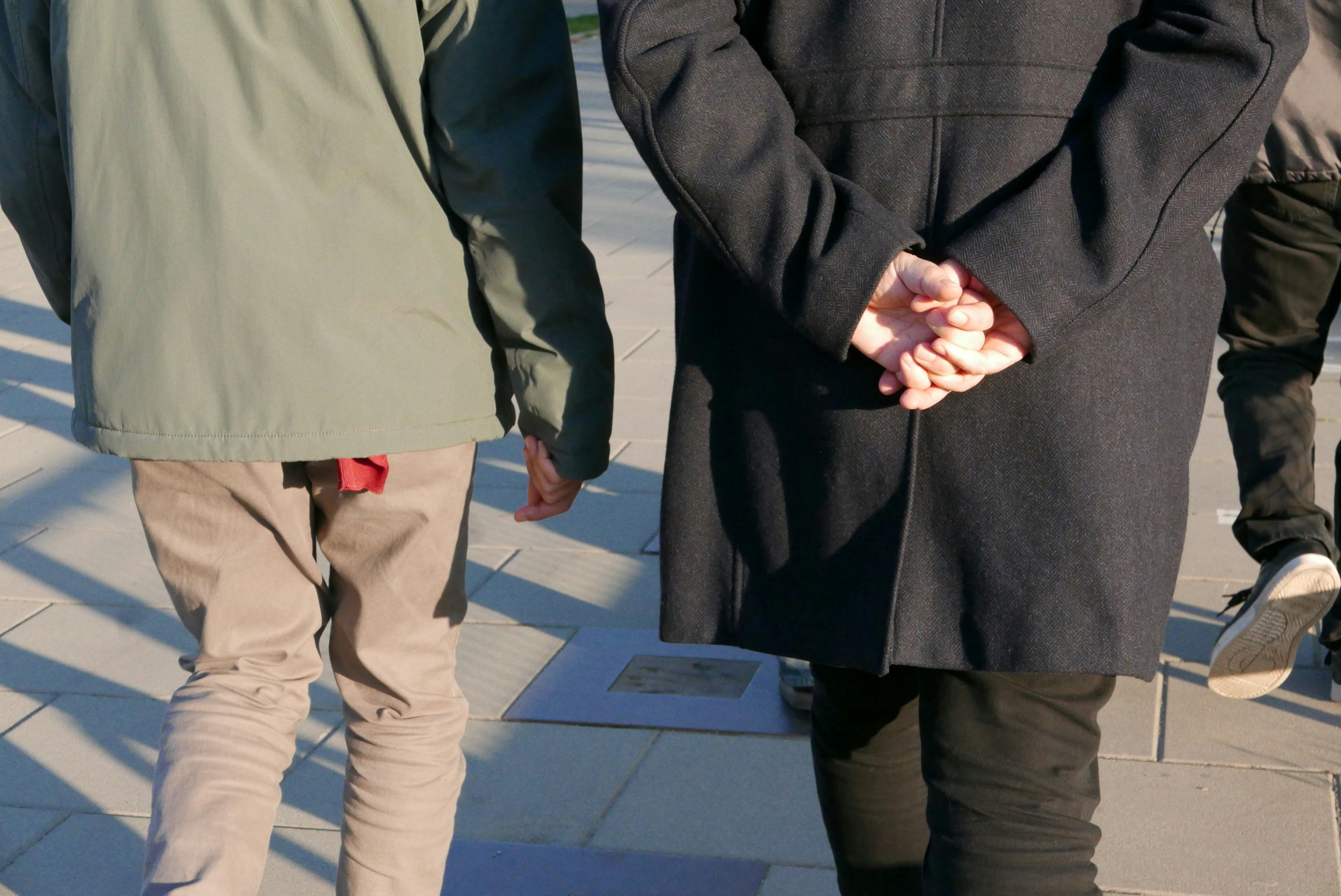 Two people walking away with hands clasped behind back.
