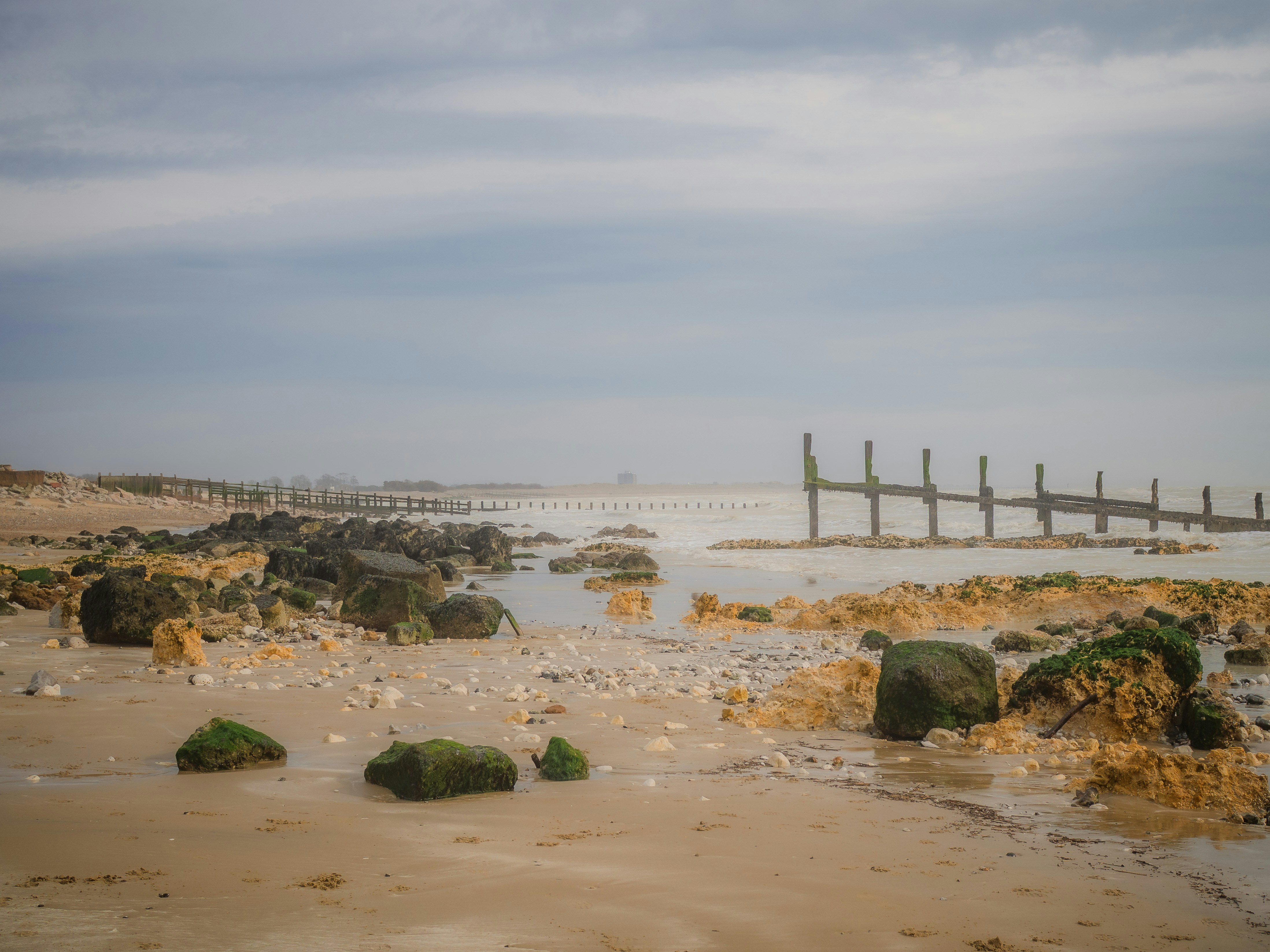 Deserted Strip of Sea: A Distant Pier Emerges Beyond Mossy Rocks