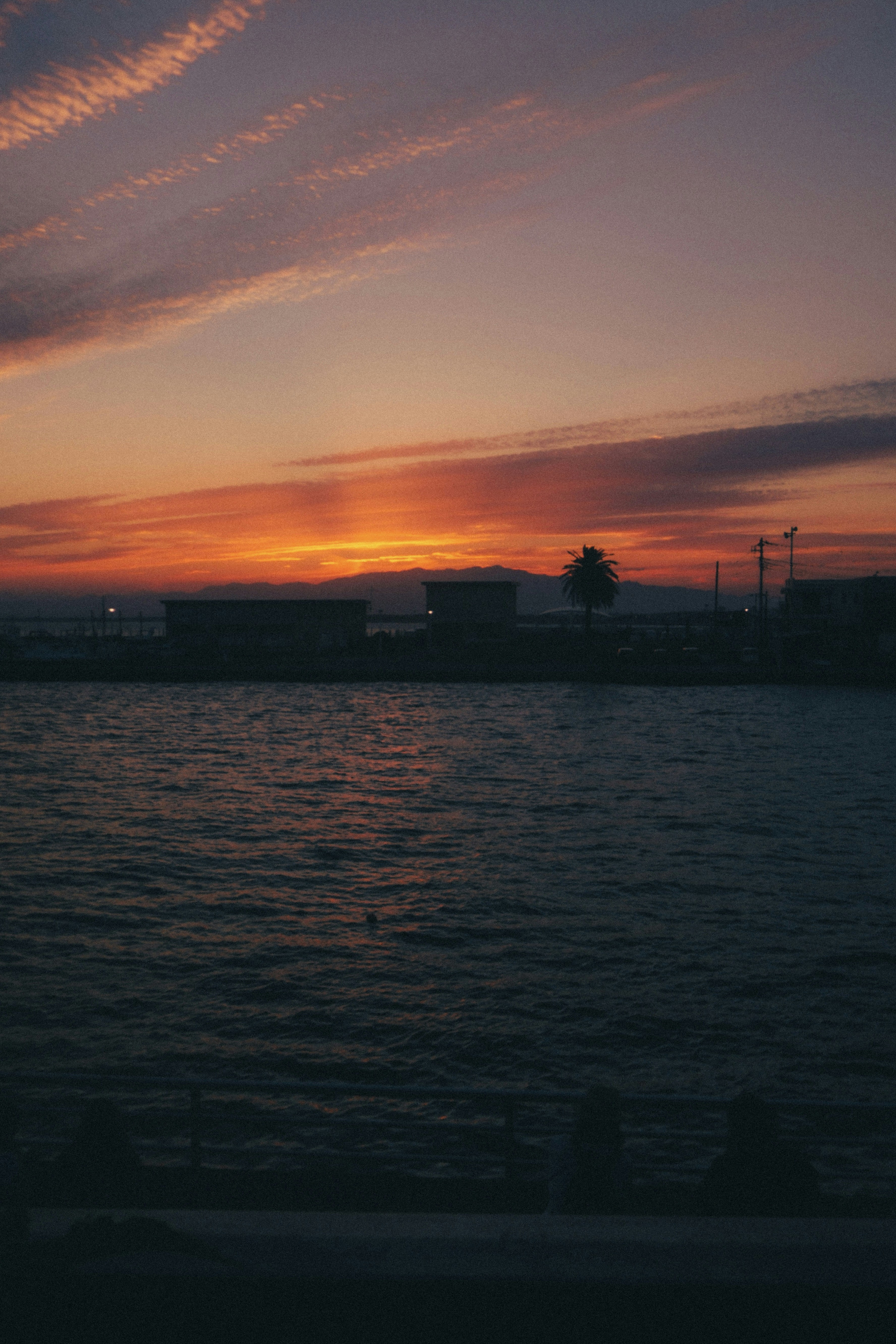 A vibrant sunset over dark water with silhouetted land.