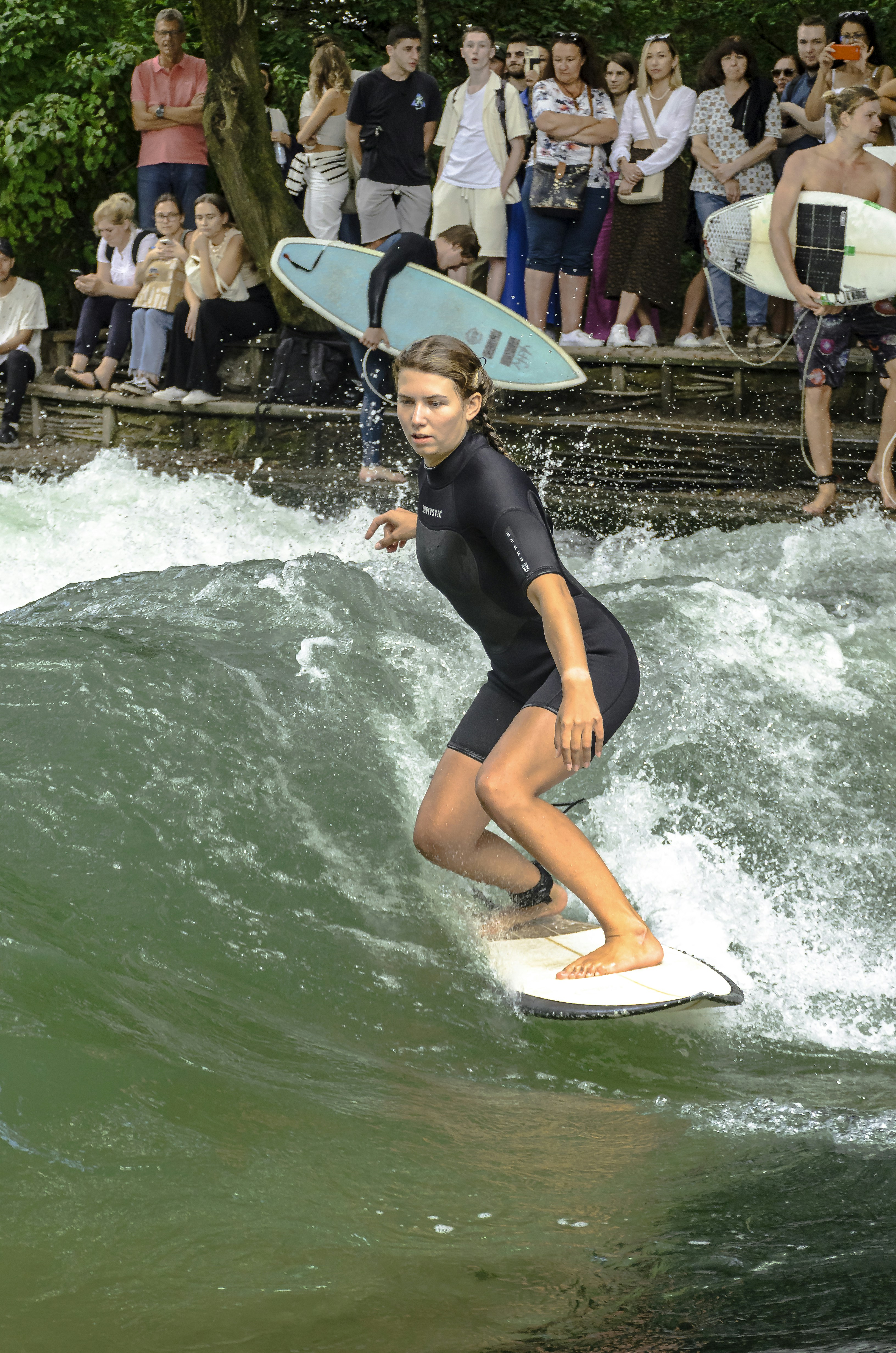 Surfer in Black: Carving a Carved White Wake as Spectators Watch