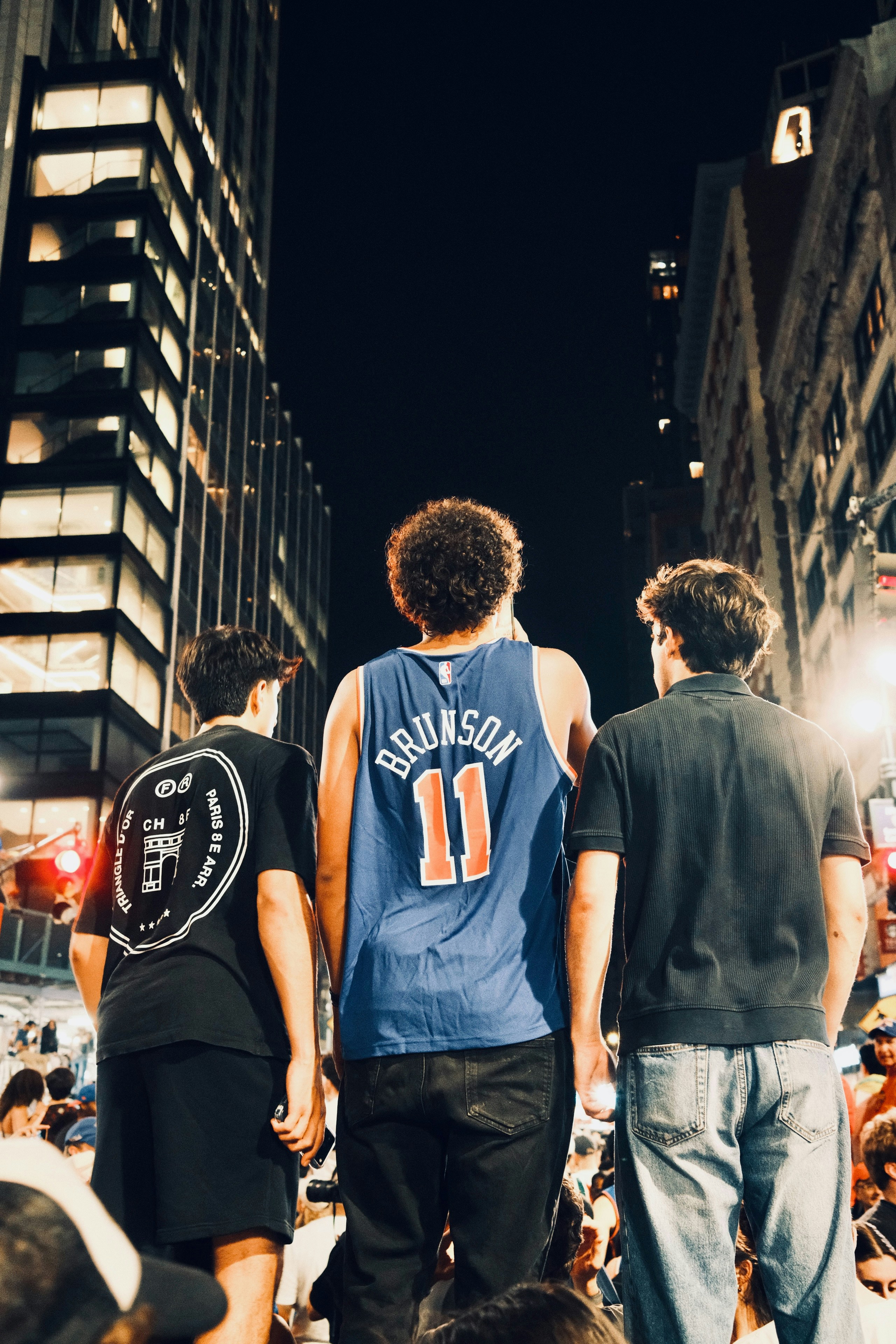 Three men in a crowd looking up at city buildings.