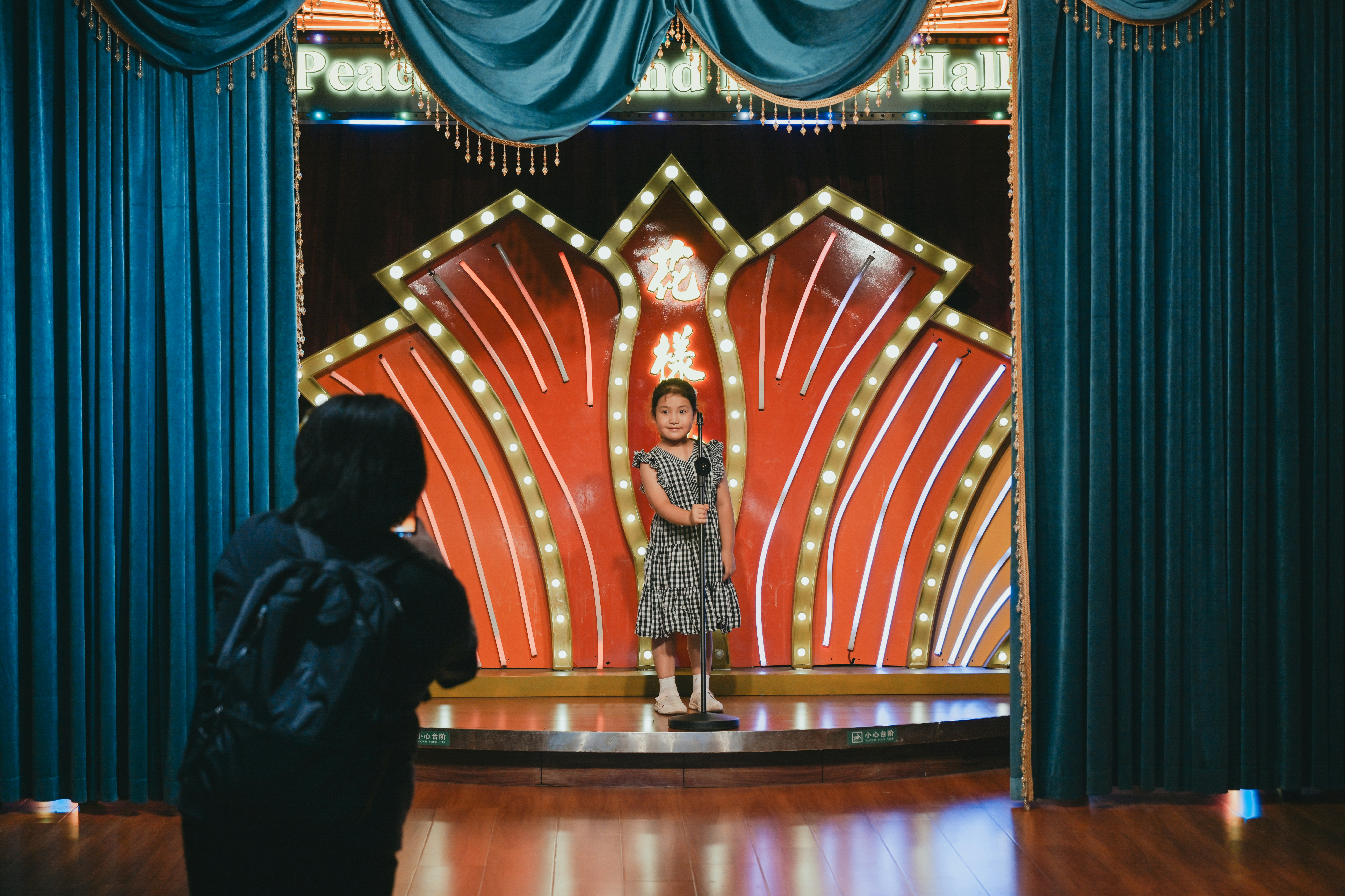 A person photographs a child posing on a lit stage.