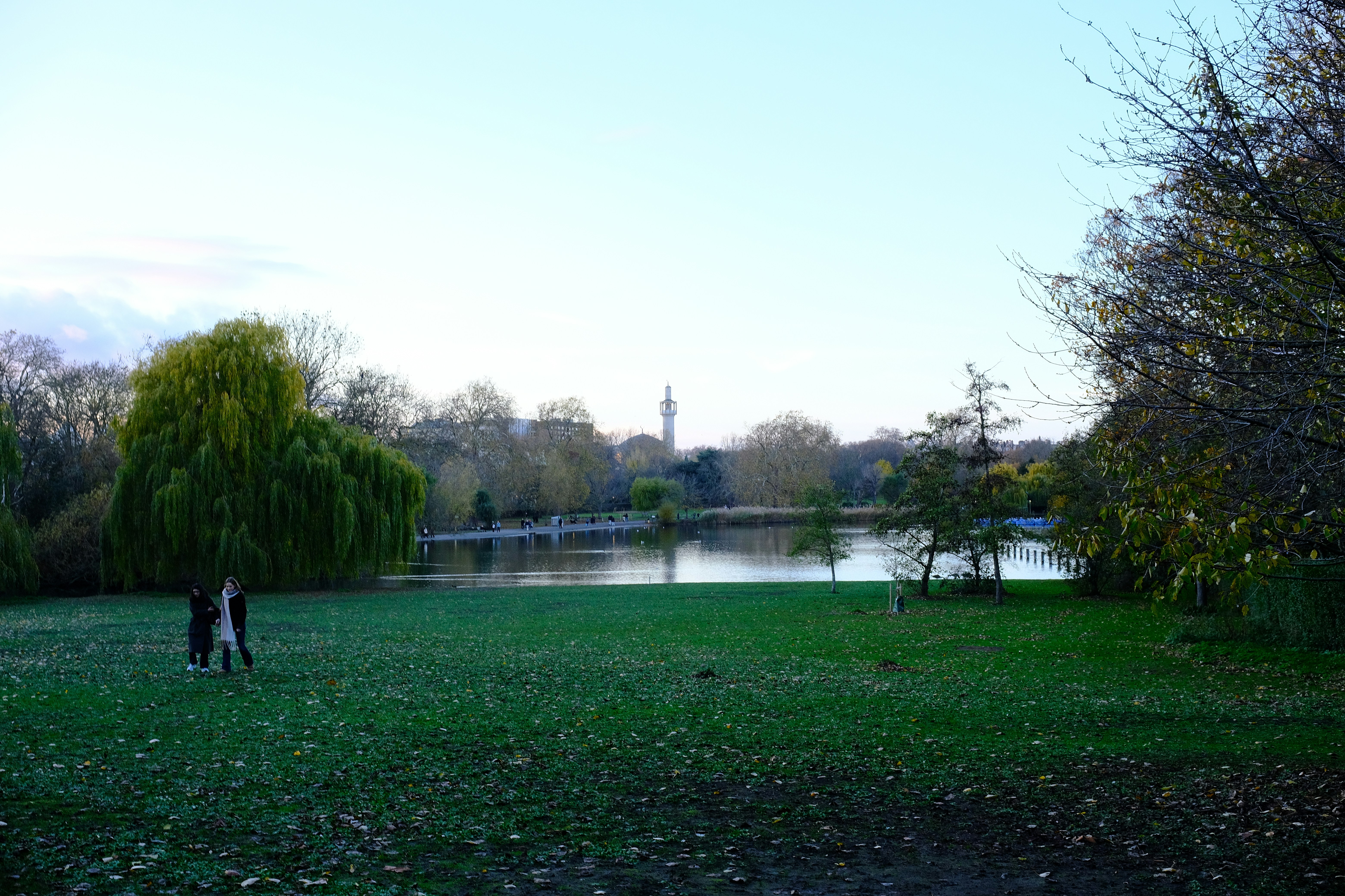 People with stroller near a tranquil city park pond at dusk