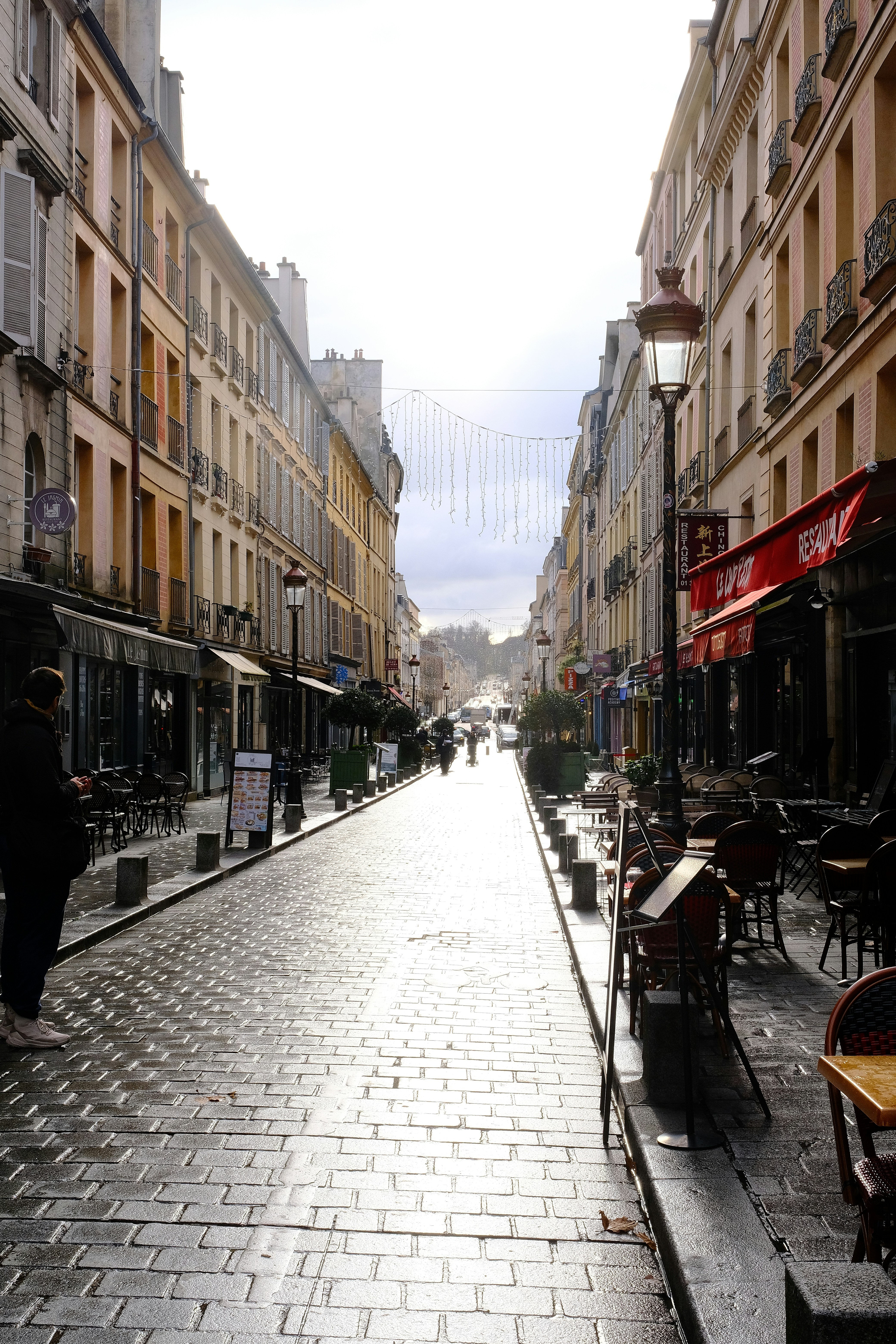 A cobblestone street lined with buildings and outdoor cafes.